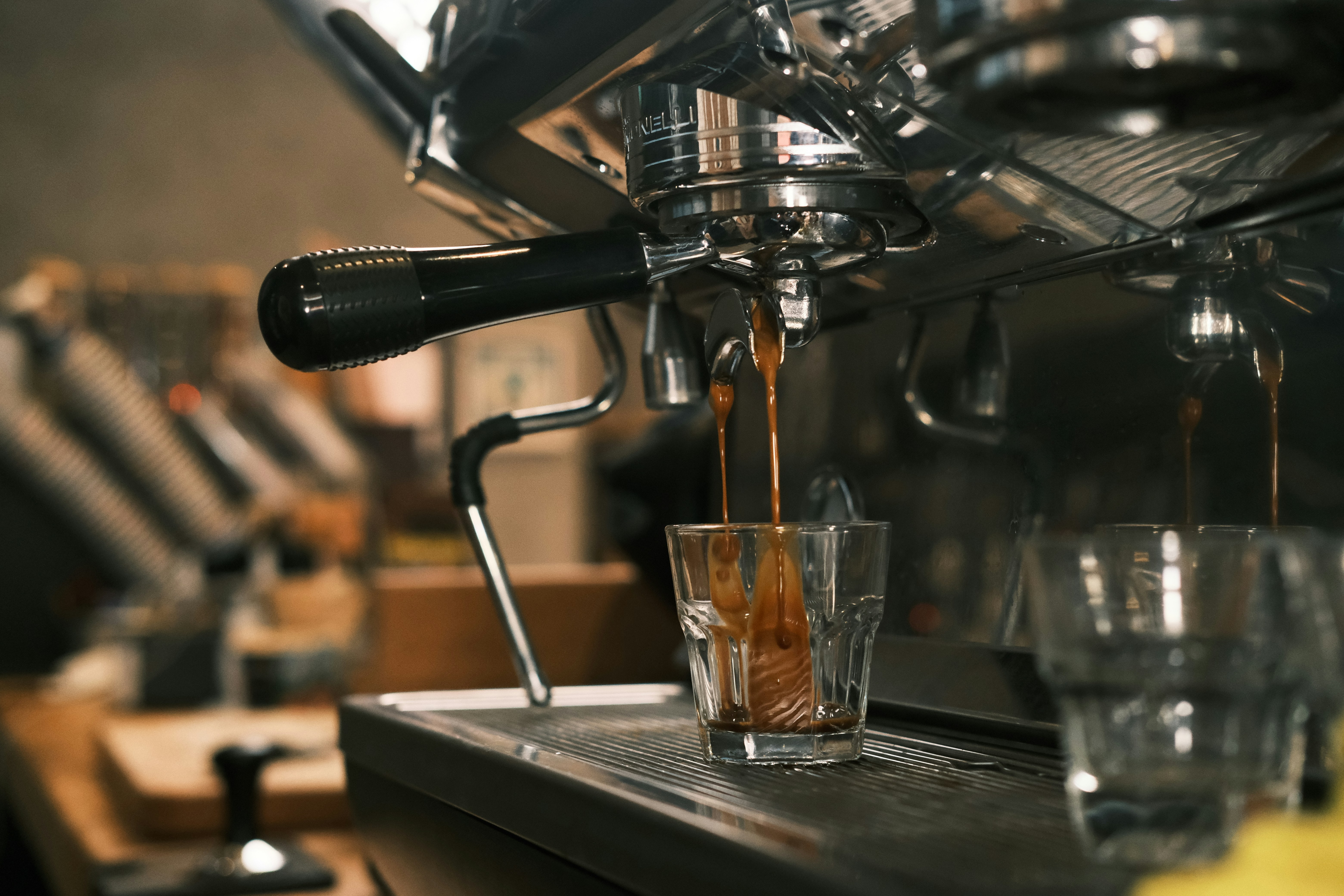 Espresso streams gracefully into a glass beneath the gleaming chrome of a coffee machine, set against warm ambient café lighting.