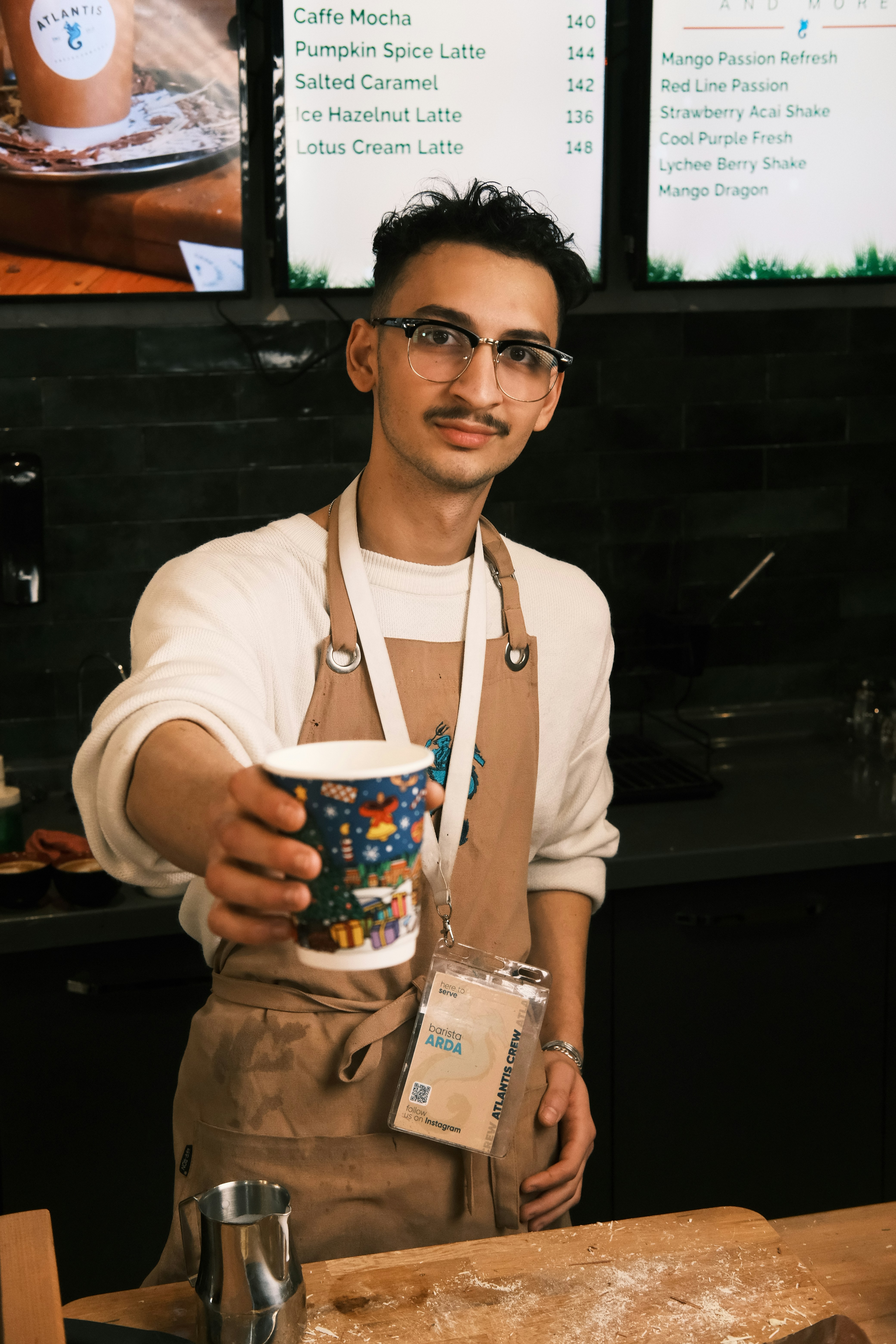 Hand-delivered warmth: A barista extends a festive cup in a cozy café