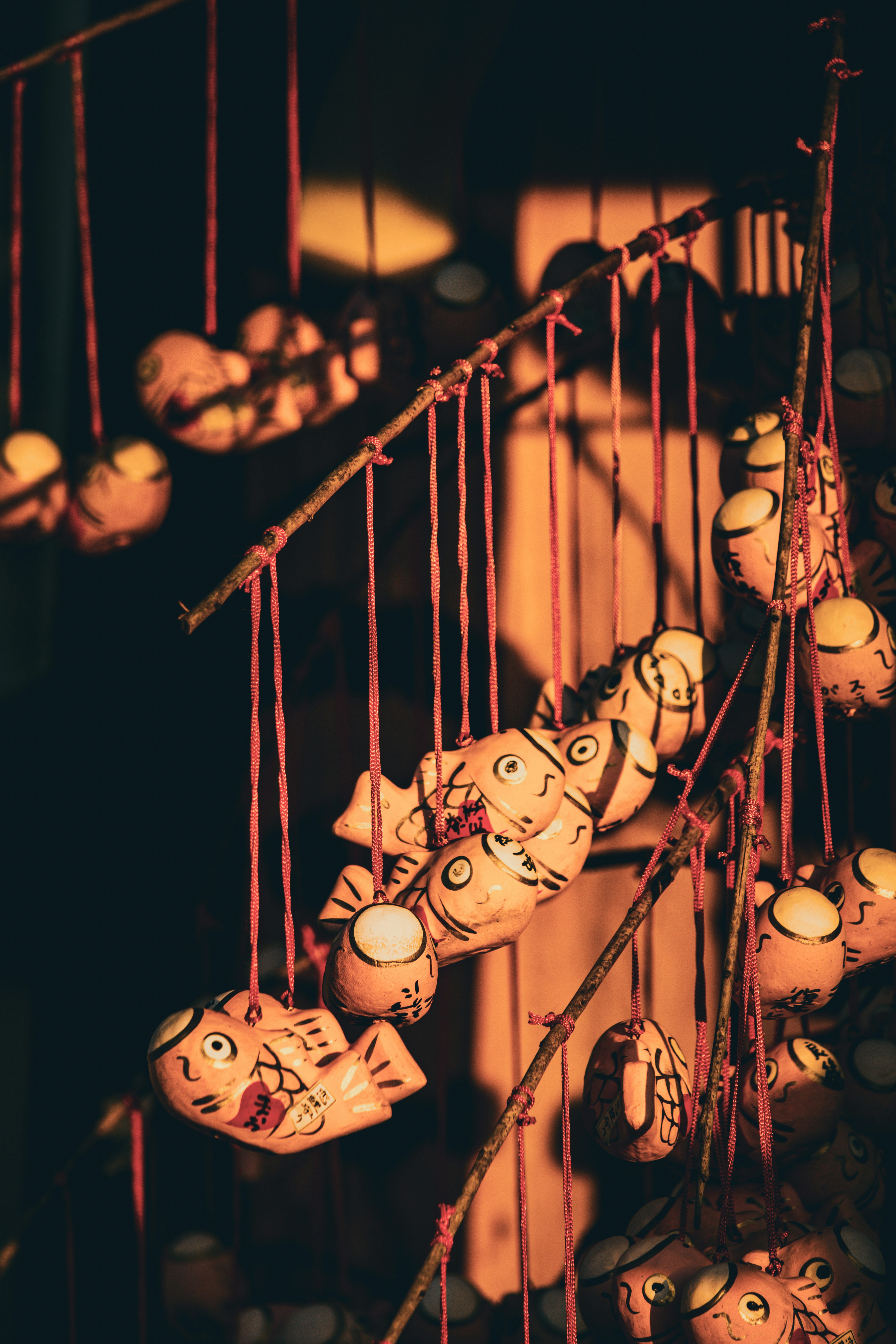 Hanging wooden fish figurines adorned with playful designs, illuminated by warm sunlight. The interplay of light and shadow creates a dynamic visual experience.