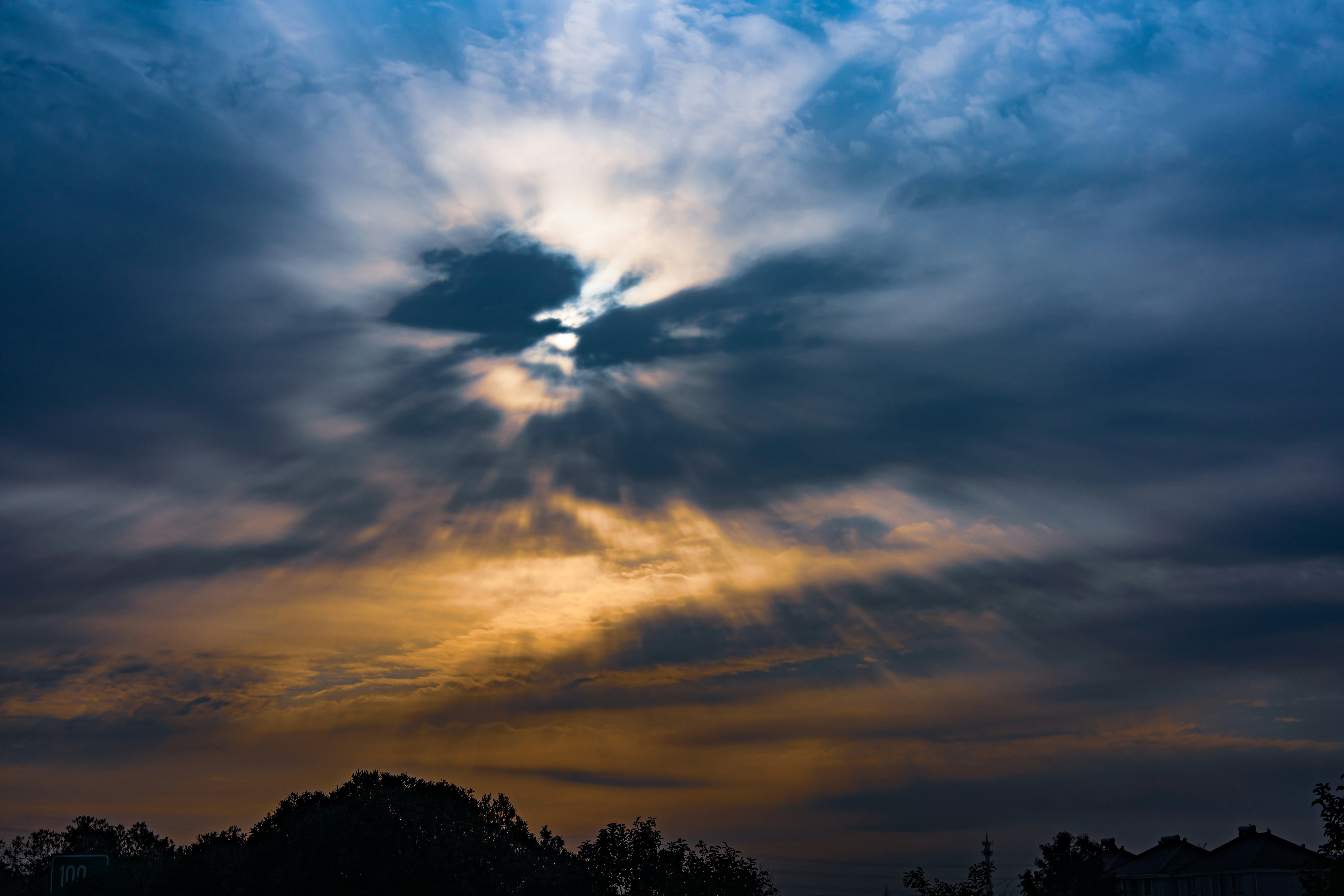 Crown of Light: Sunpierce Through Storm-Soft Clouds Over a Quiet Suburban Horizon
