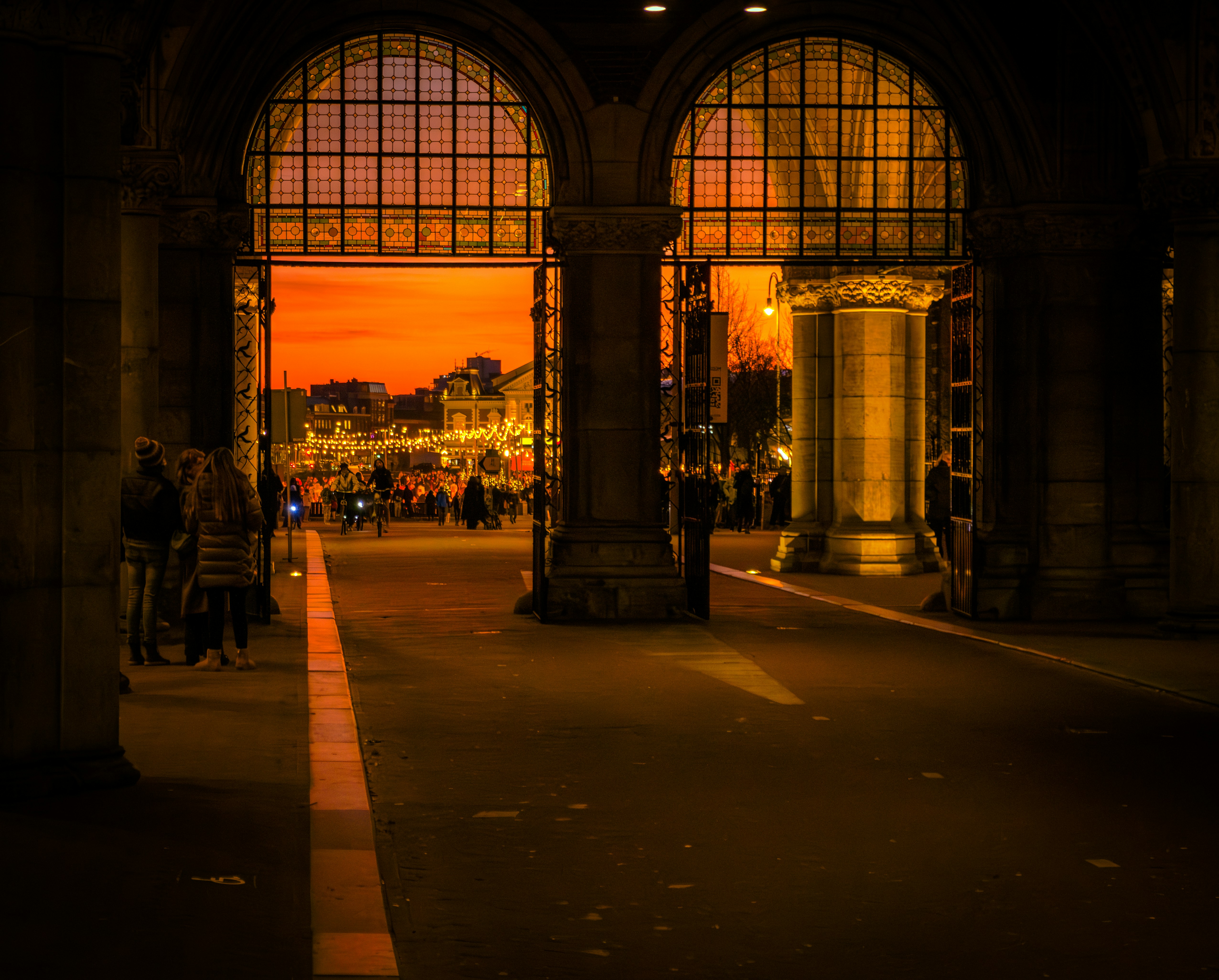 Illuminated archway framing a bustling street scene at dusk, with warm hues of sunset reflecting off the buildings. 