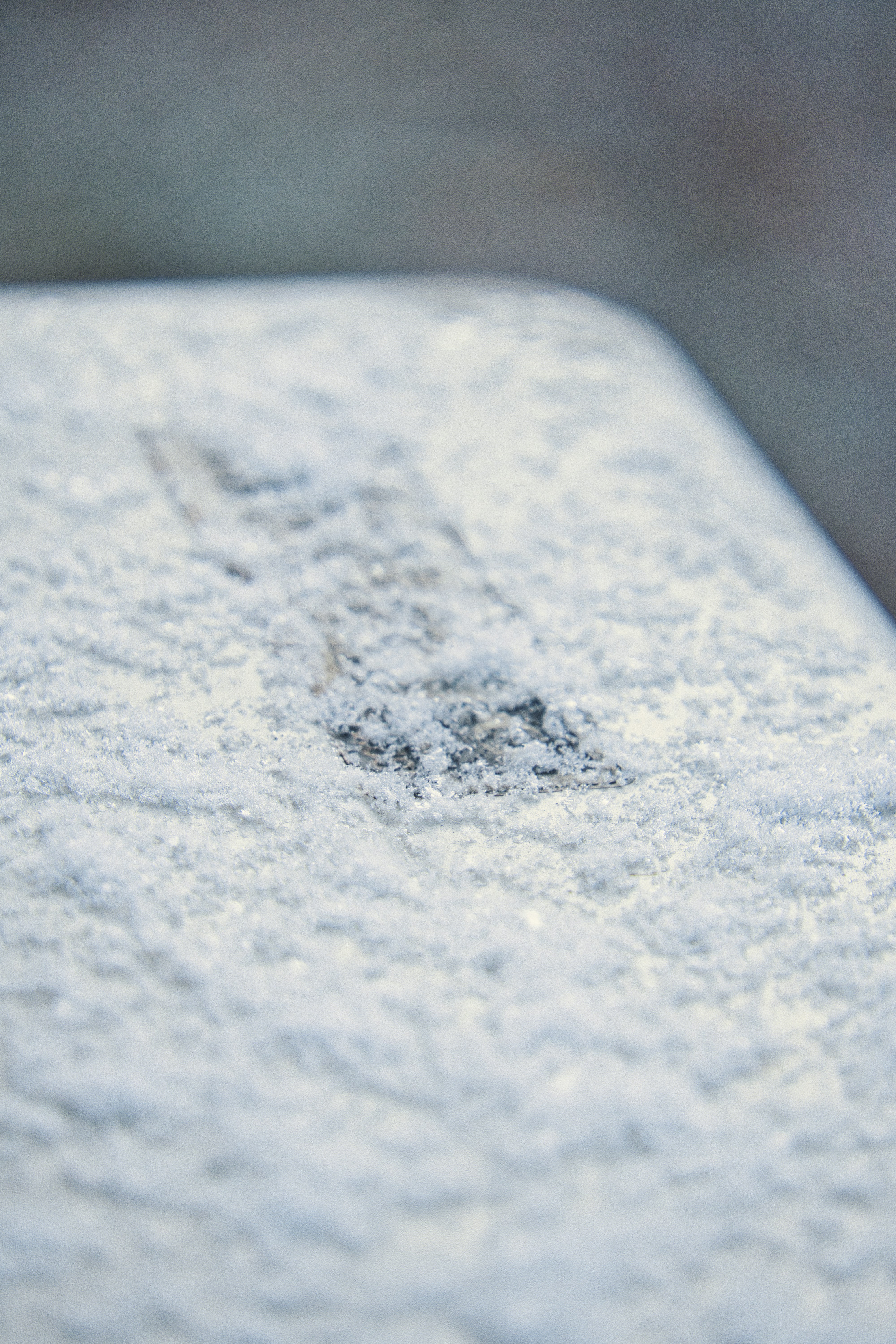 Close-up photograph of a snow-dusted flat surface with a subtle dark imprint.