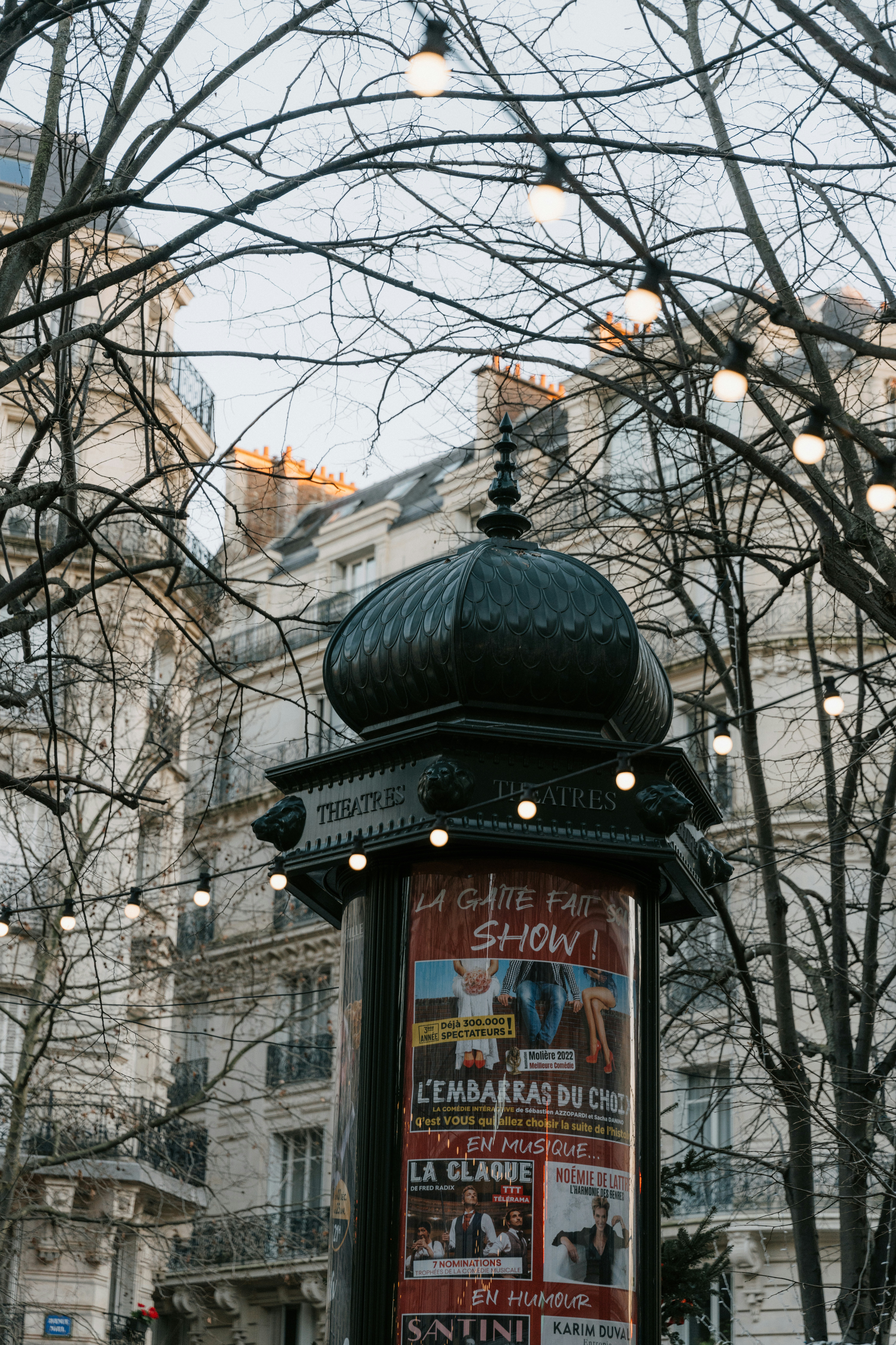 Lanterns Over Ledger: The Ornate Poster Kiosk on a Winter City Street