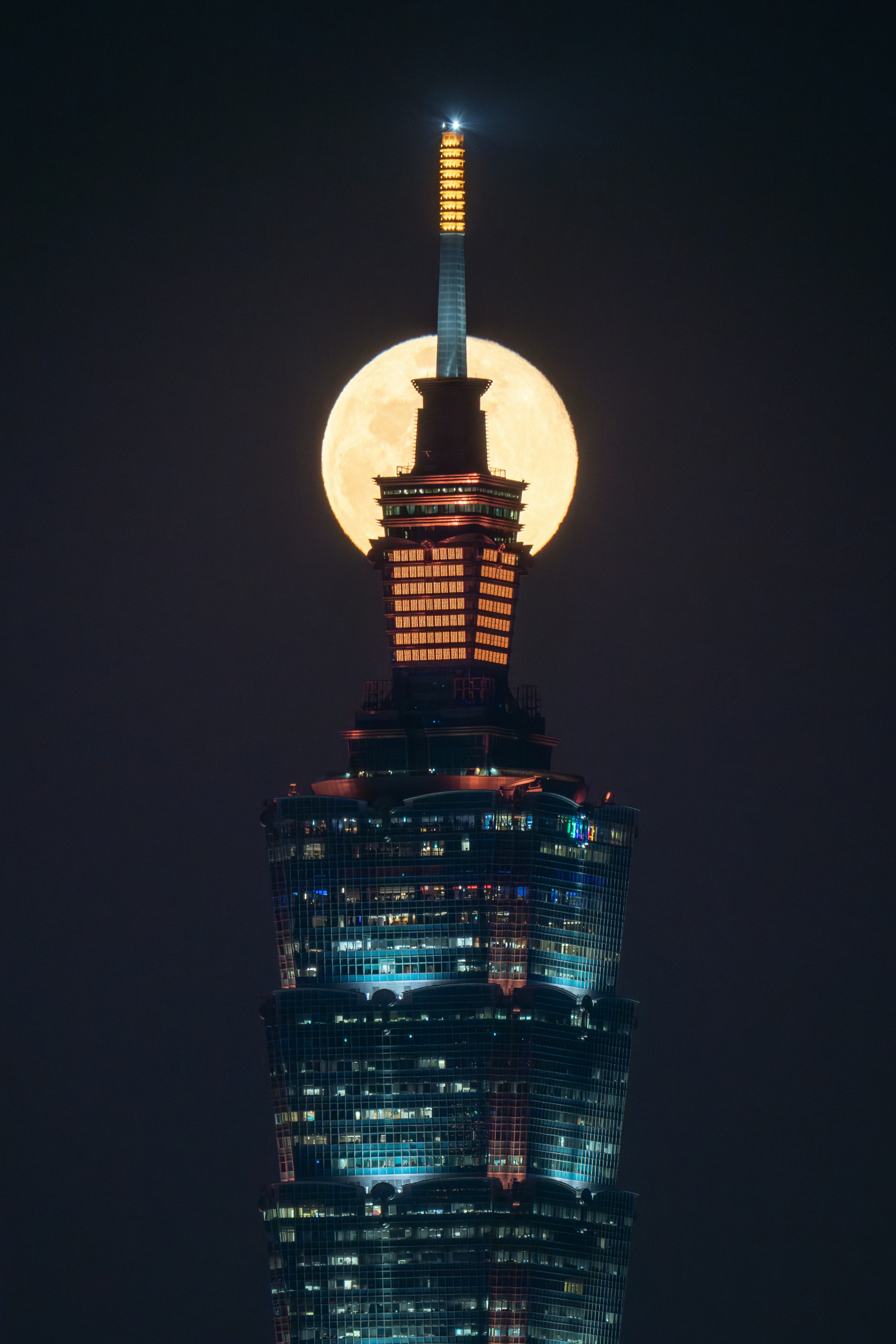 A full moon rises over the top of a skyscraper