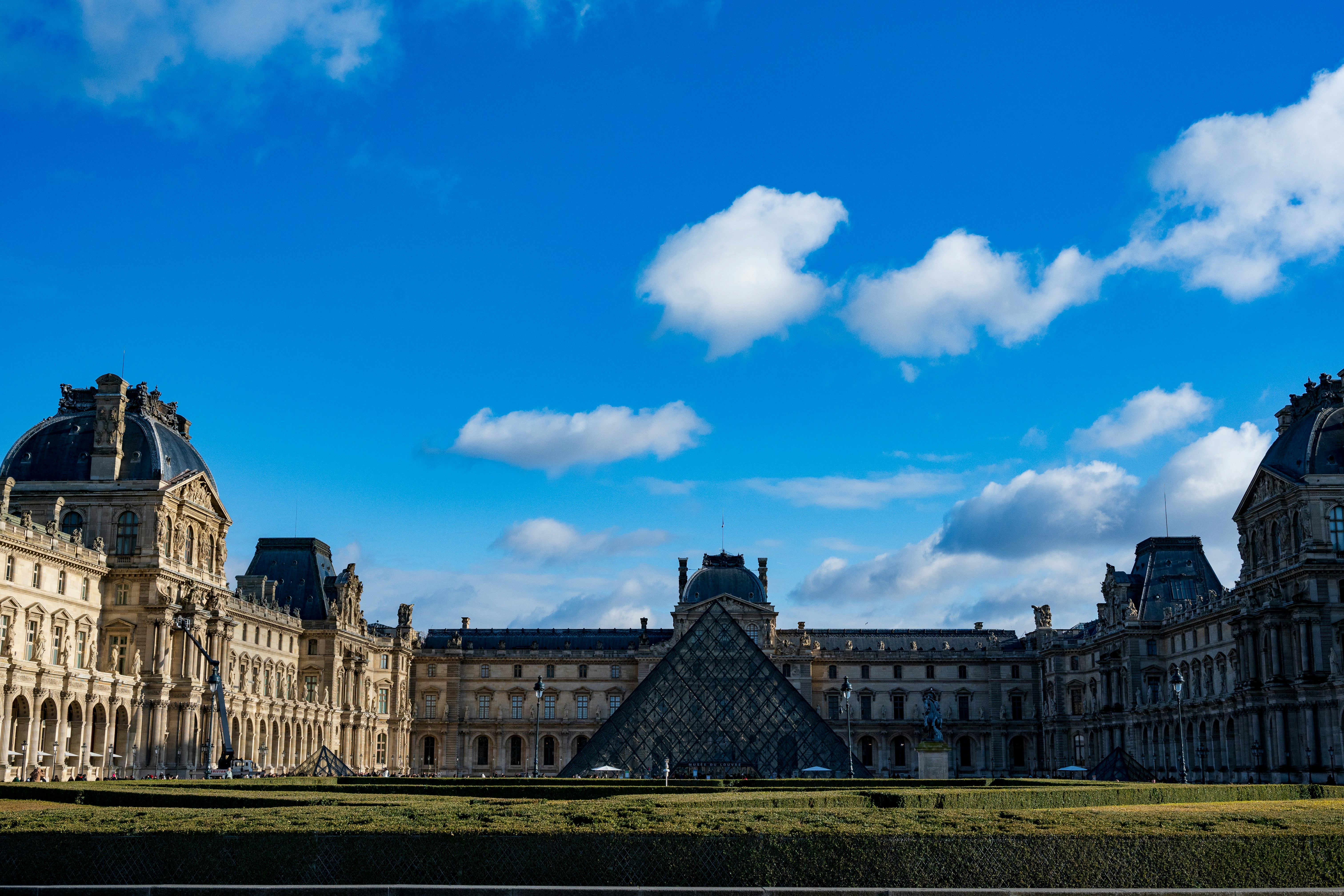 Louvre Museum's architecture under a vibrant blue sky with scattered clouds.