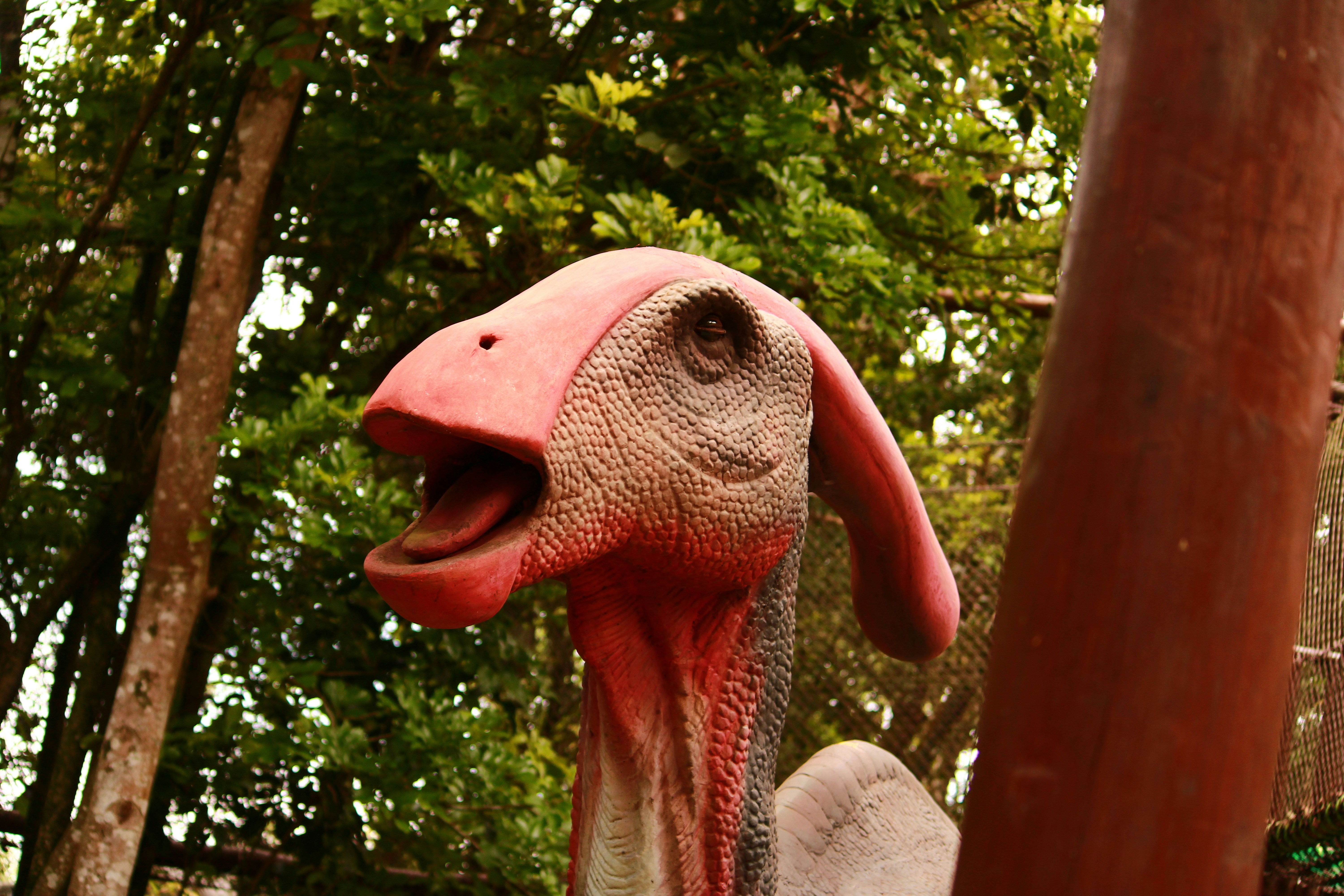 Open-Mouthed Pink Sentinel: A Dinosaur Head in a Leafy Enclosure