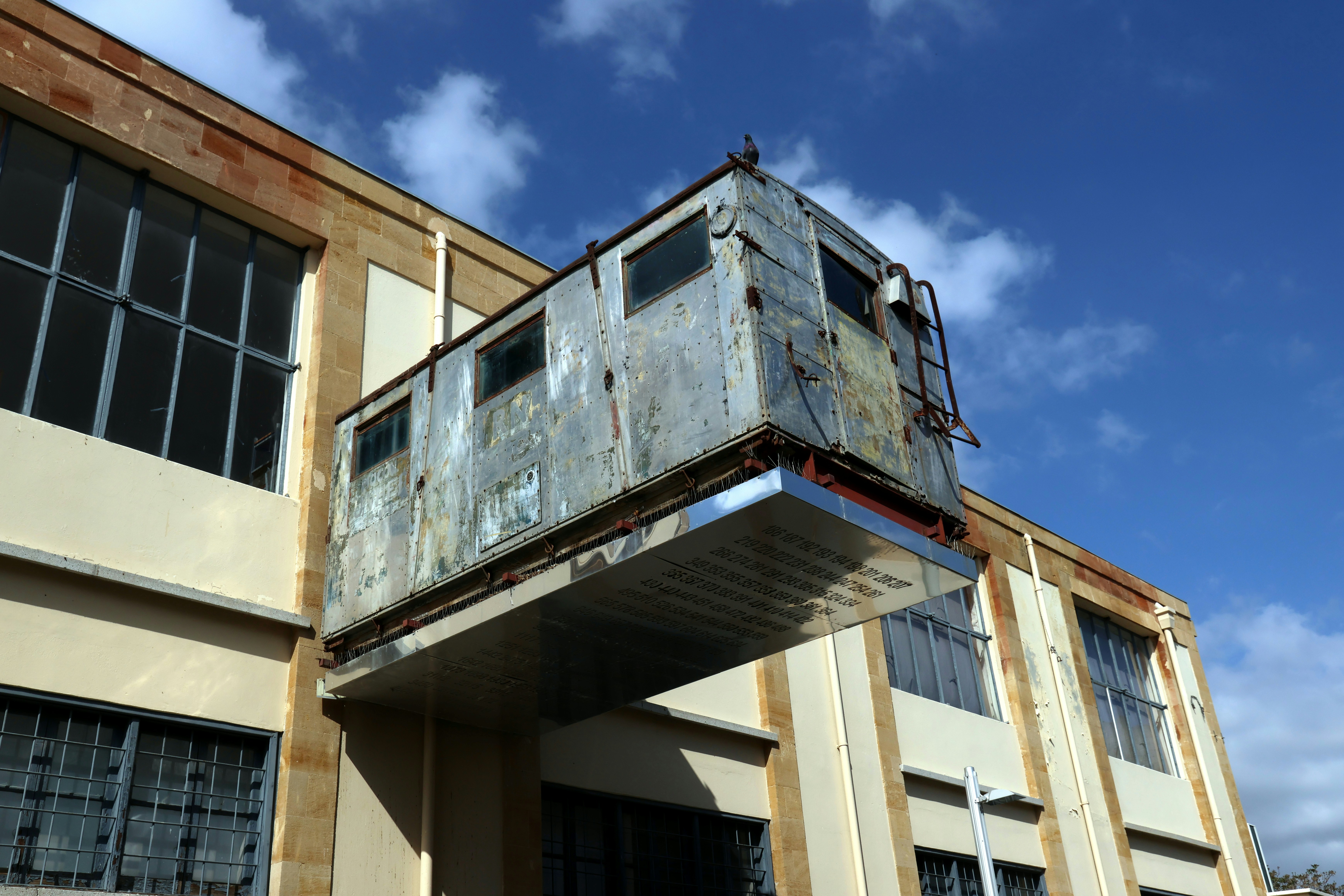 Rusting Balcony Tower Emerges from a Sunlit Factory Facade
