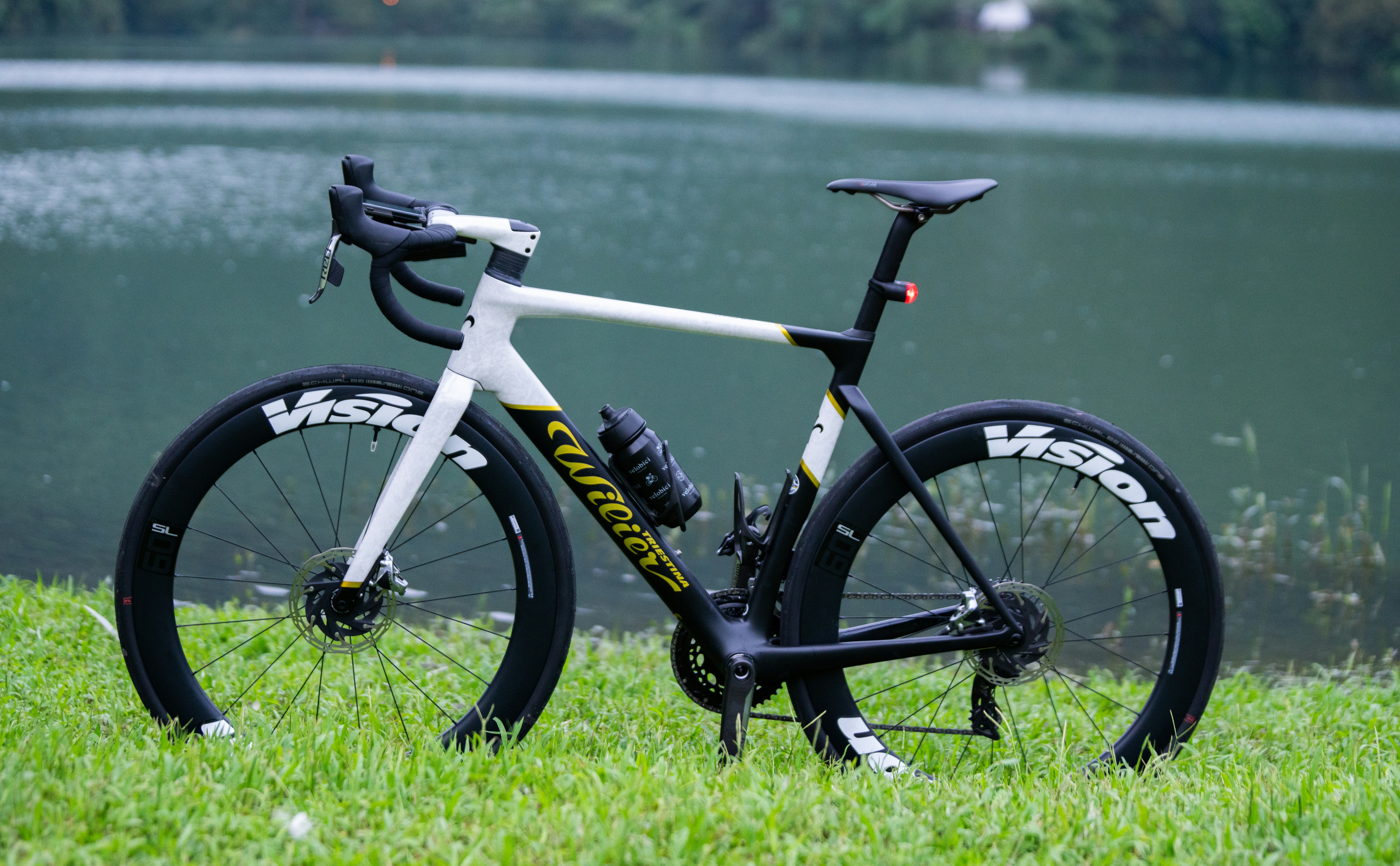 High-performance road bike with aerodynamic design resting on grass by a tranquil lake.