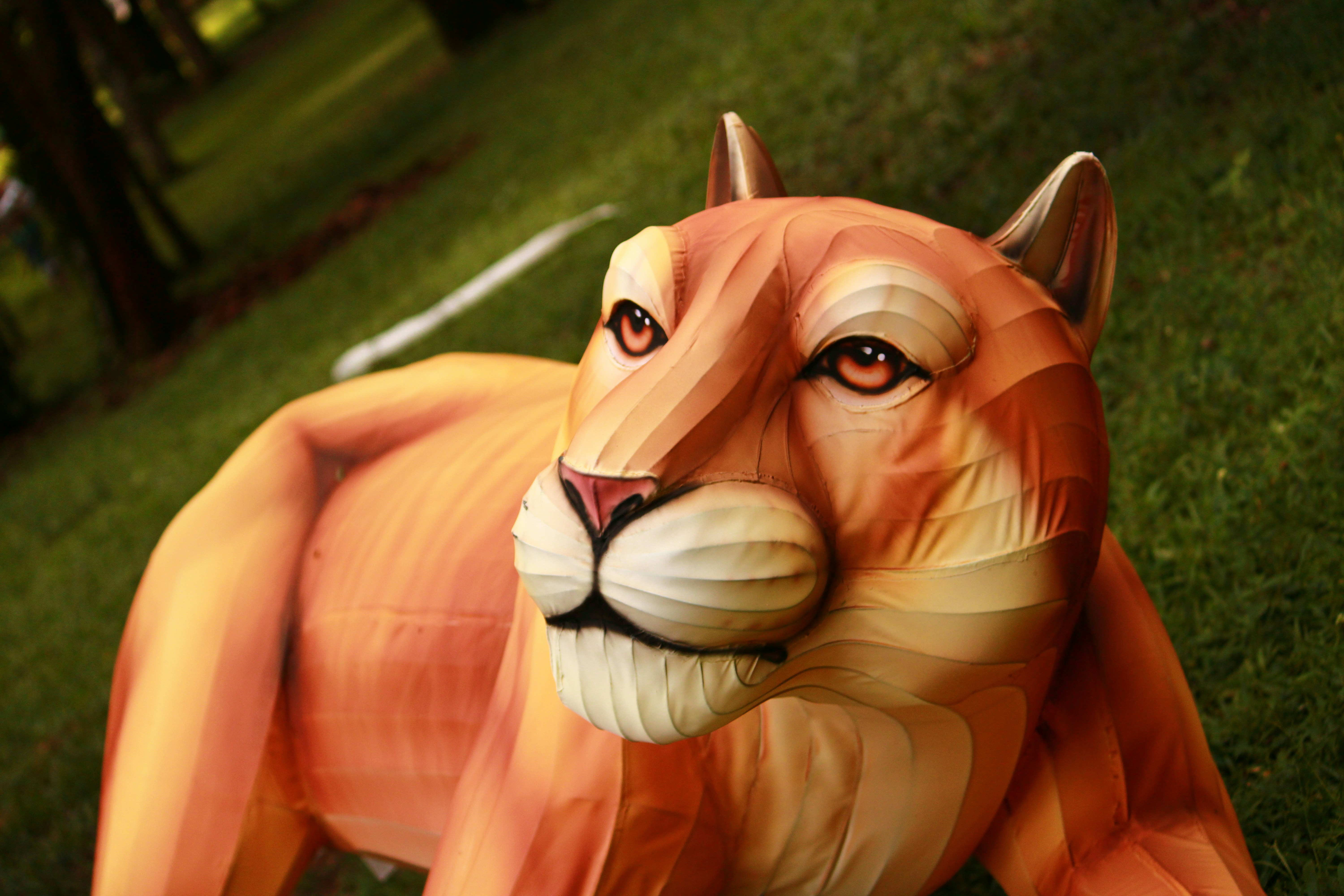 Close-up of a stylized feline sculpture with intricate detailing in a grassy park.