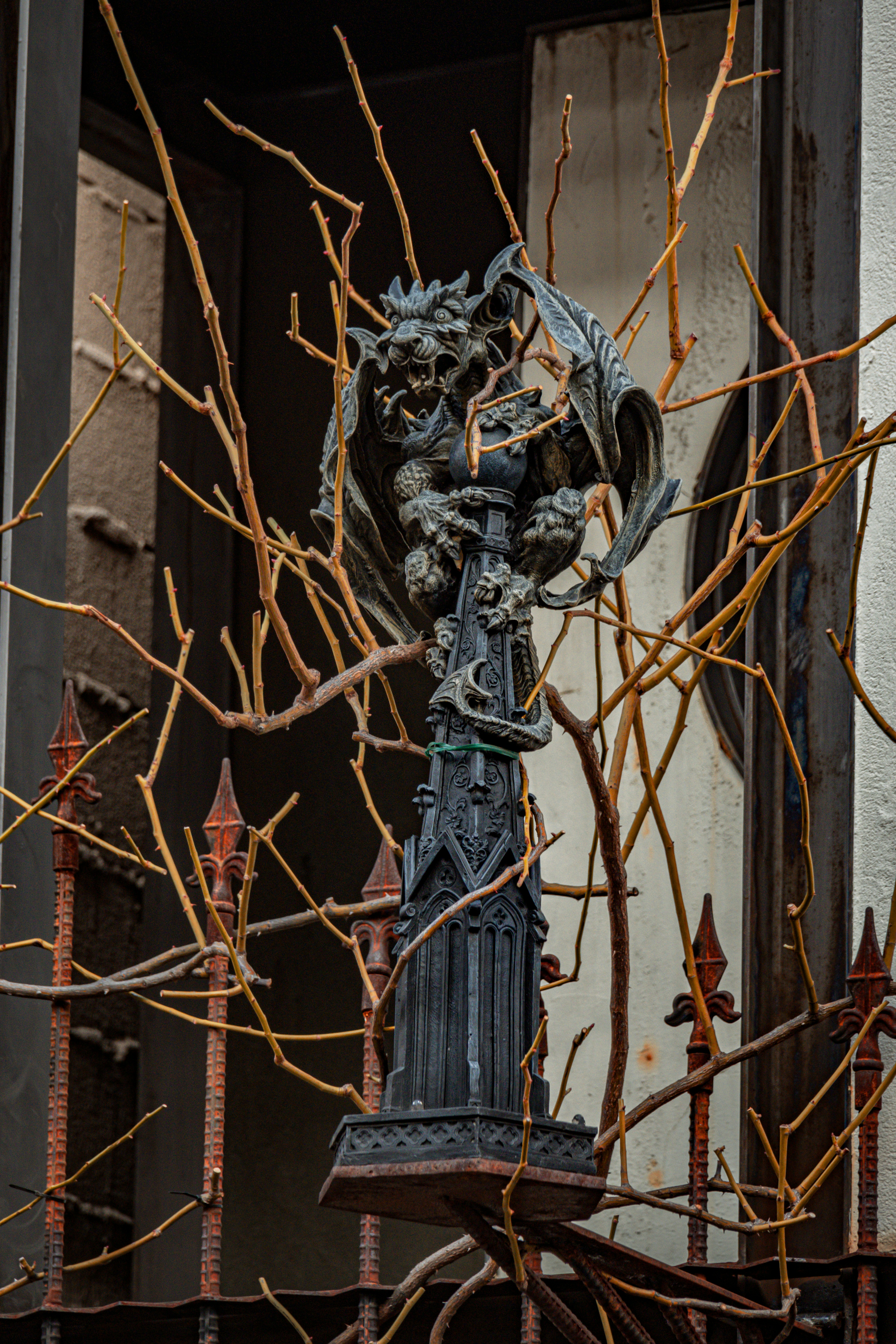 Gothic Statue Surrounded by Bare Branches Behind Iron Spikes