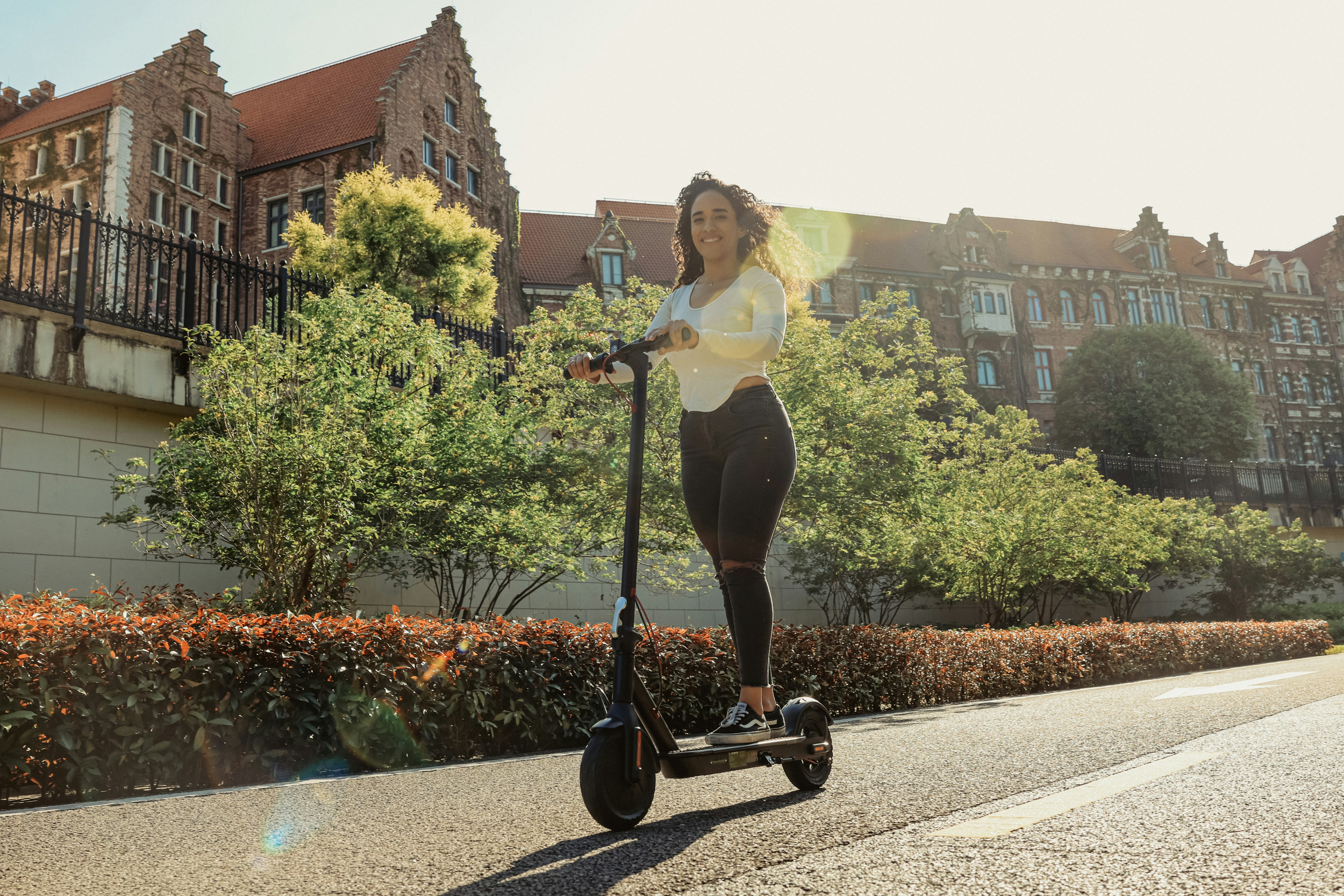 A woman riding an electric scooter down a street photo – Free Scooter ...