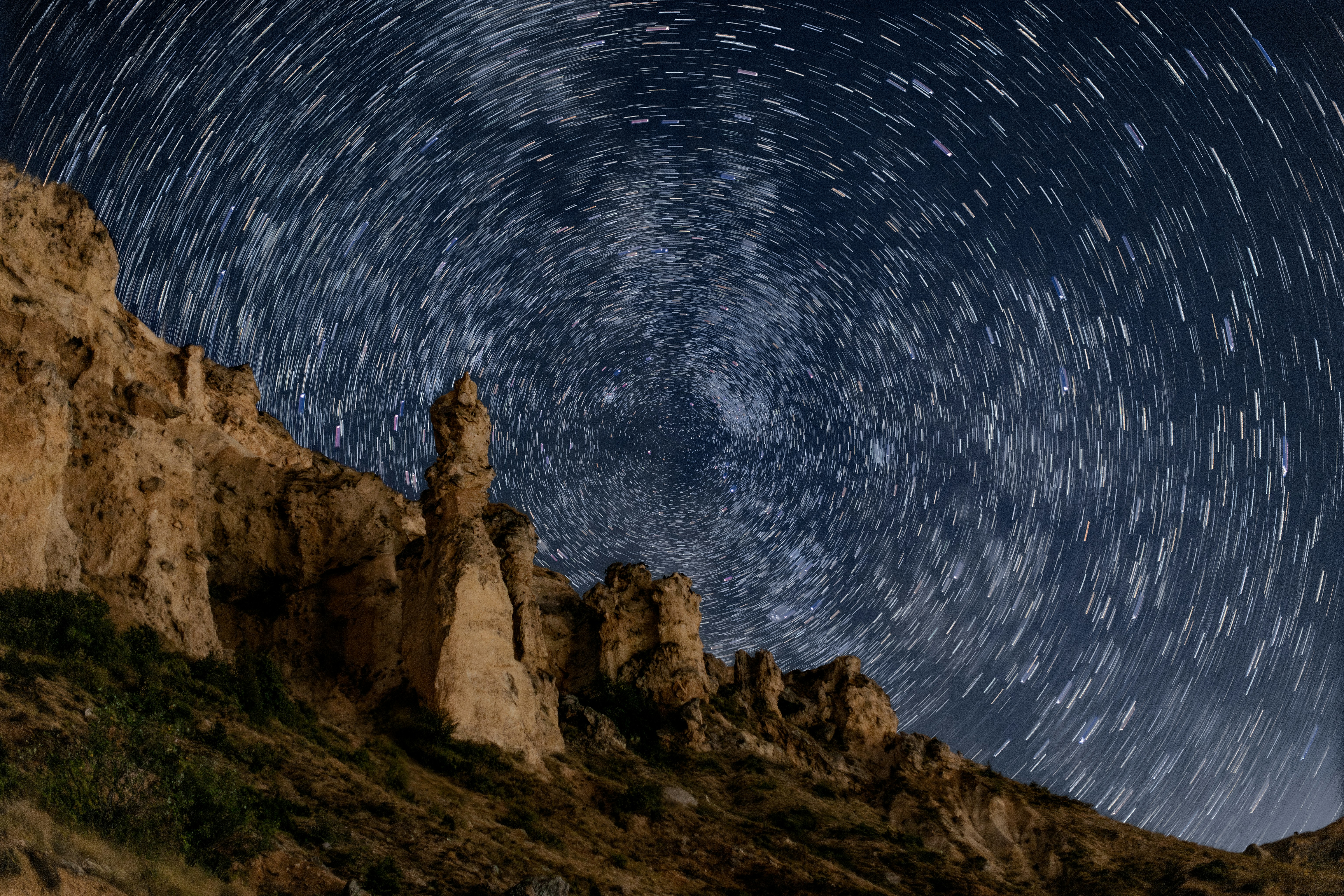 Star trails swirl around a rocky outcrop under a night sky, showcasing the movement of celestial bodies over time.