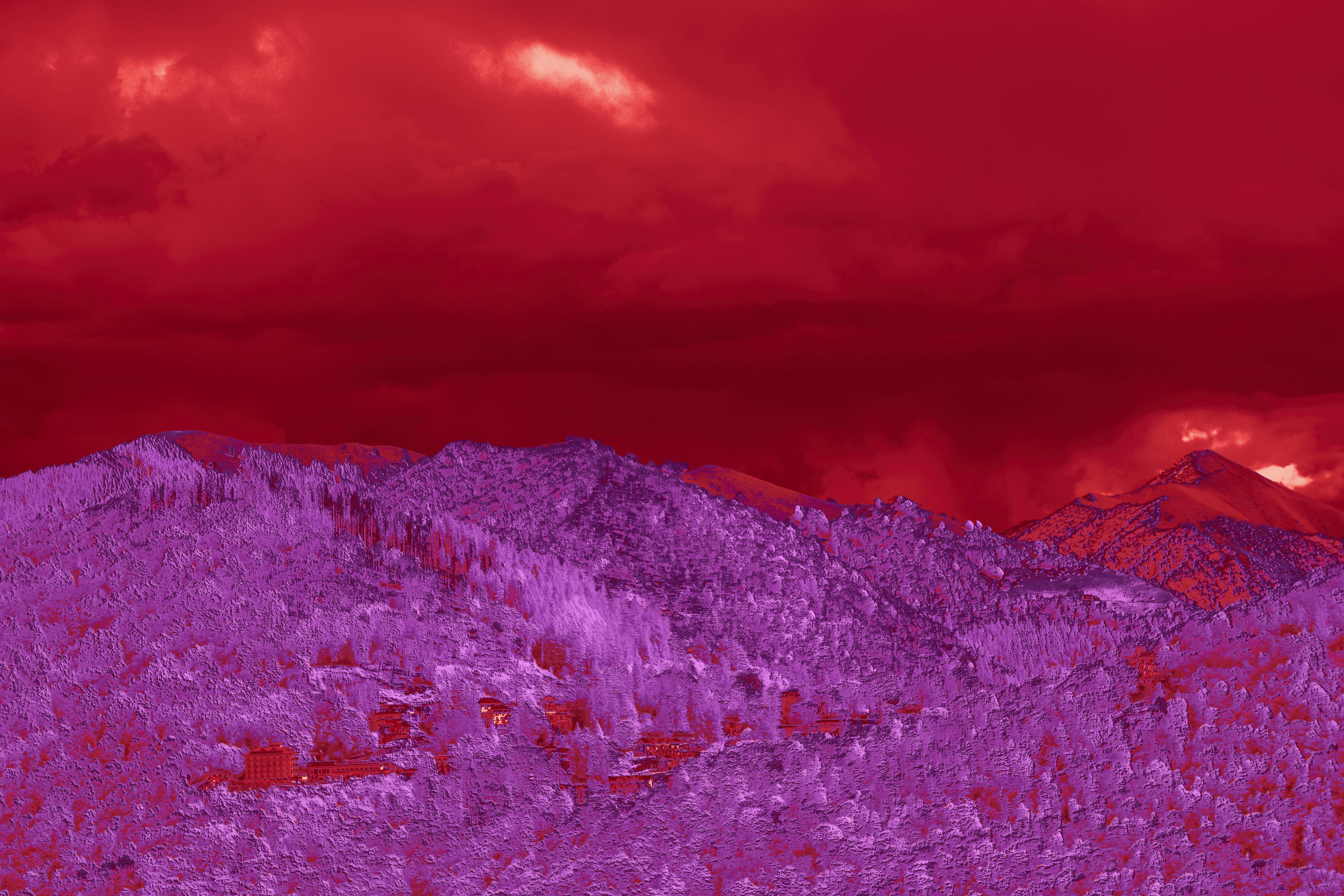 Vibrant mountains enveloped in shades of purple and red under a dramatic sky, creating an otherworldly landscape.
