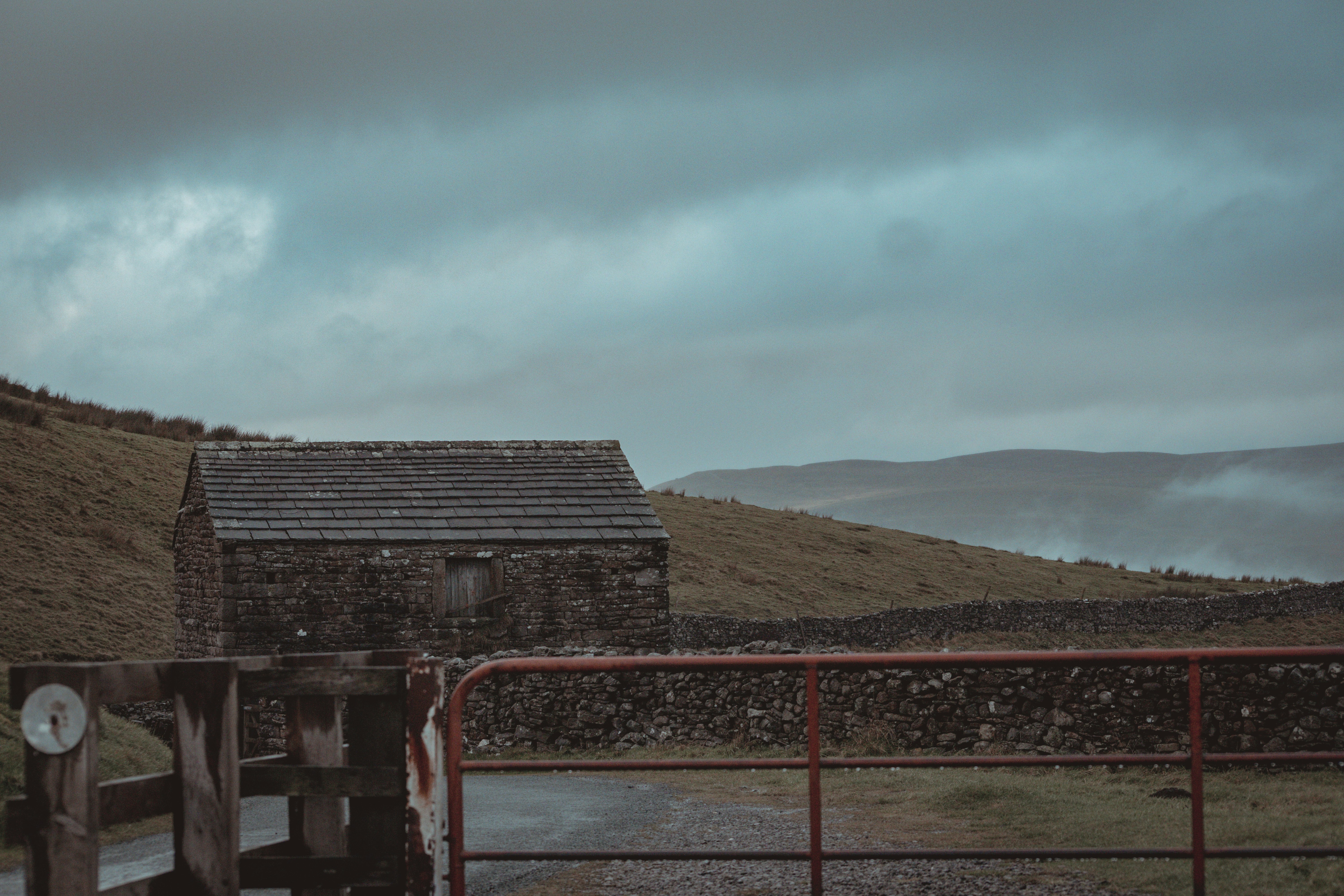 Stone barn nestled in rolling hills under a moody, overcast sky.