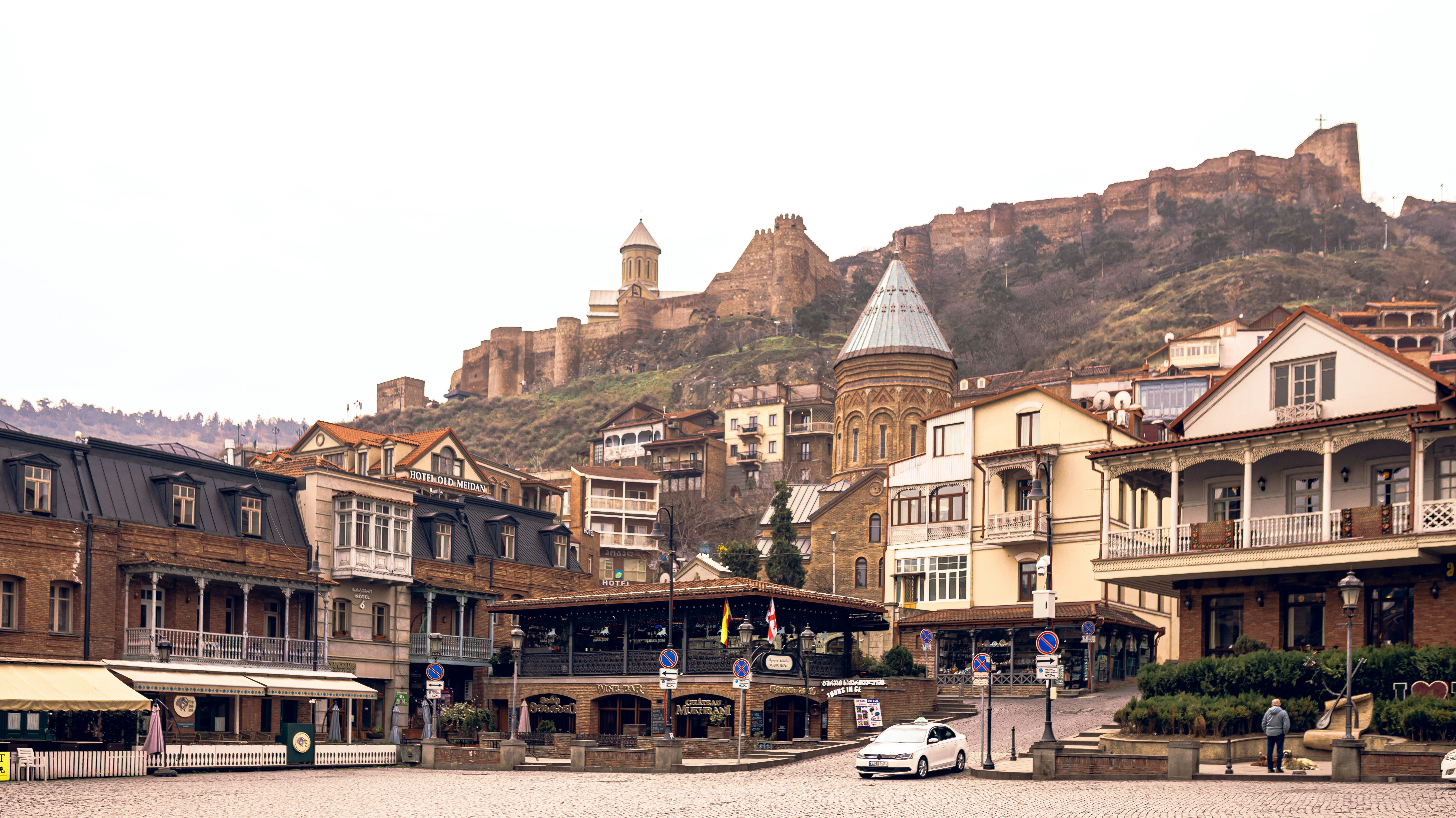 Old town buildings with a fortress on a hill in Tbilisi, showcasing diverse architecture under a cloudy sky.