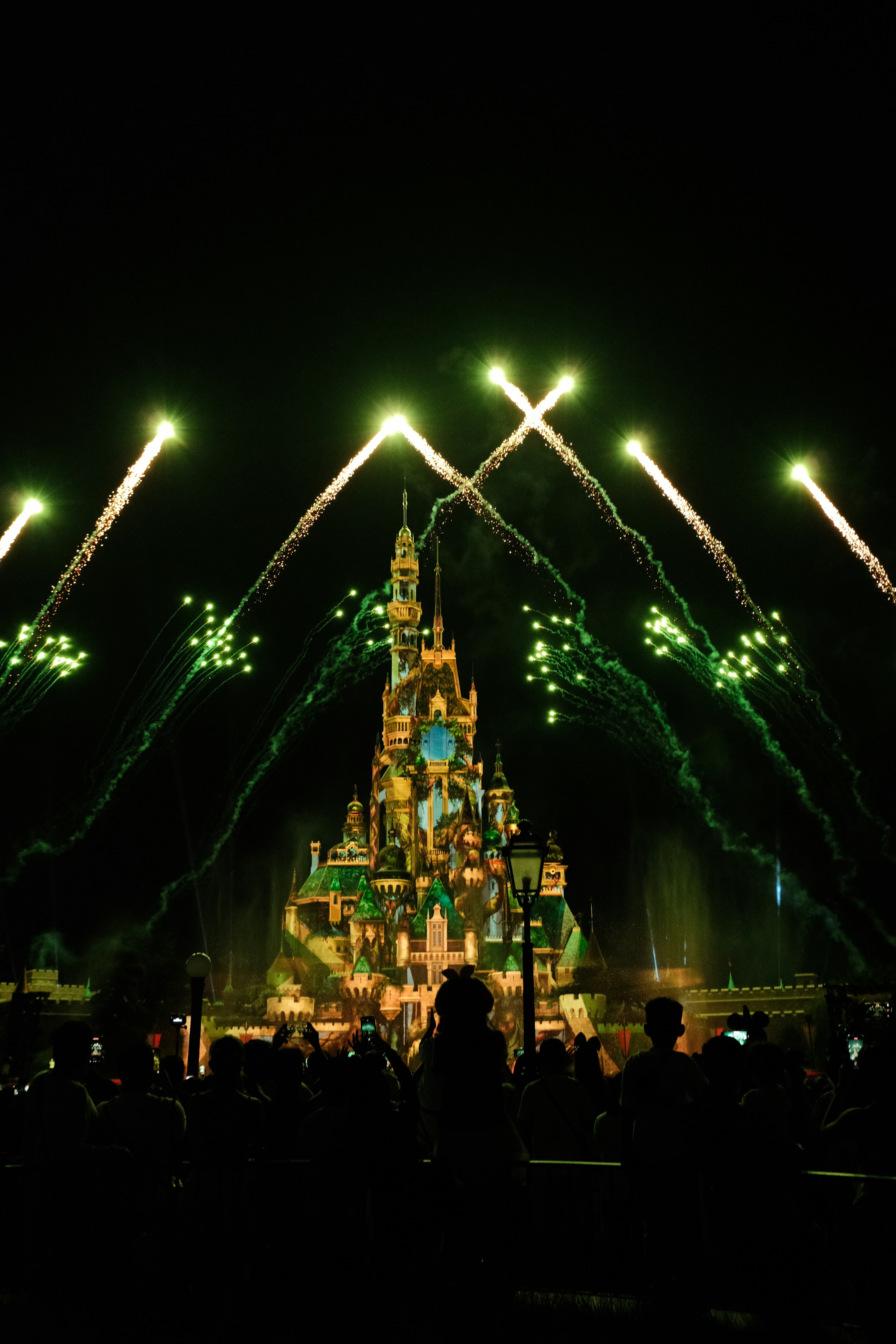 Fireworks illuminate a grand castle at night, creating a magical atmosphere as spectators watch in awe.
