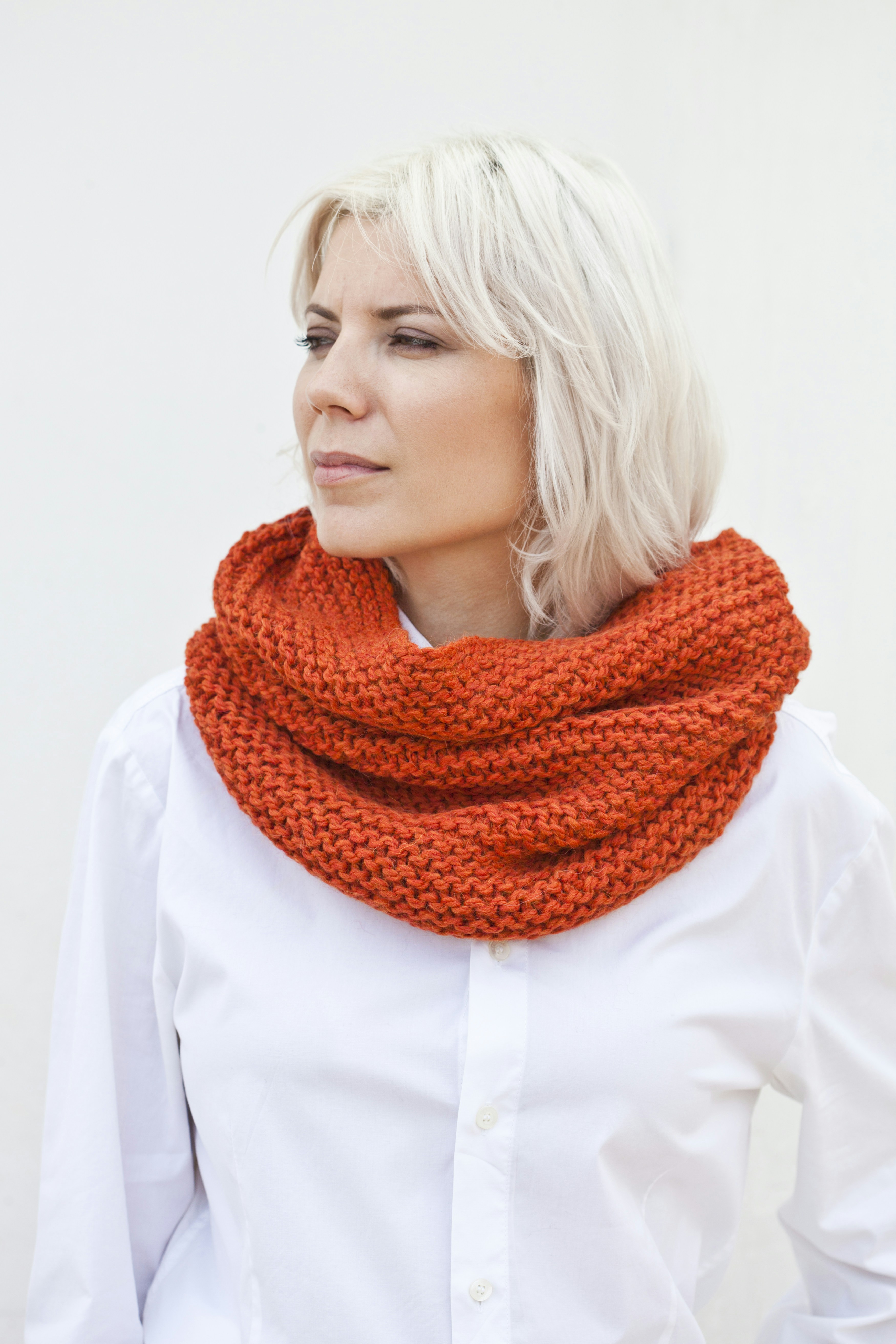 Heat in Knit: Portrait of a Woman in a Chunky Orange Scarf Against a Pale Backdrop