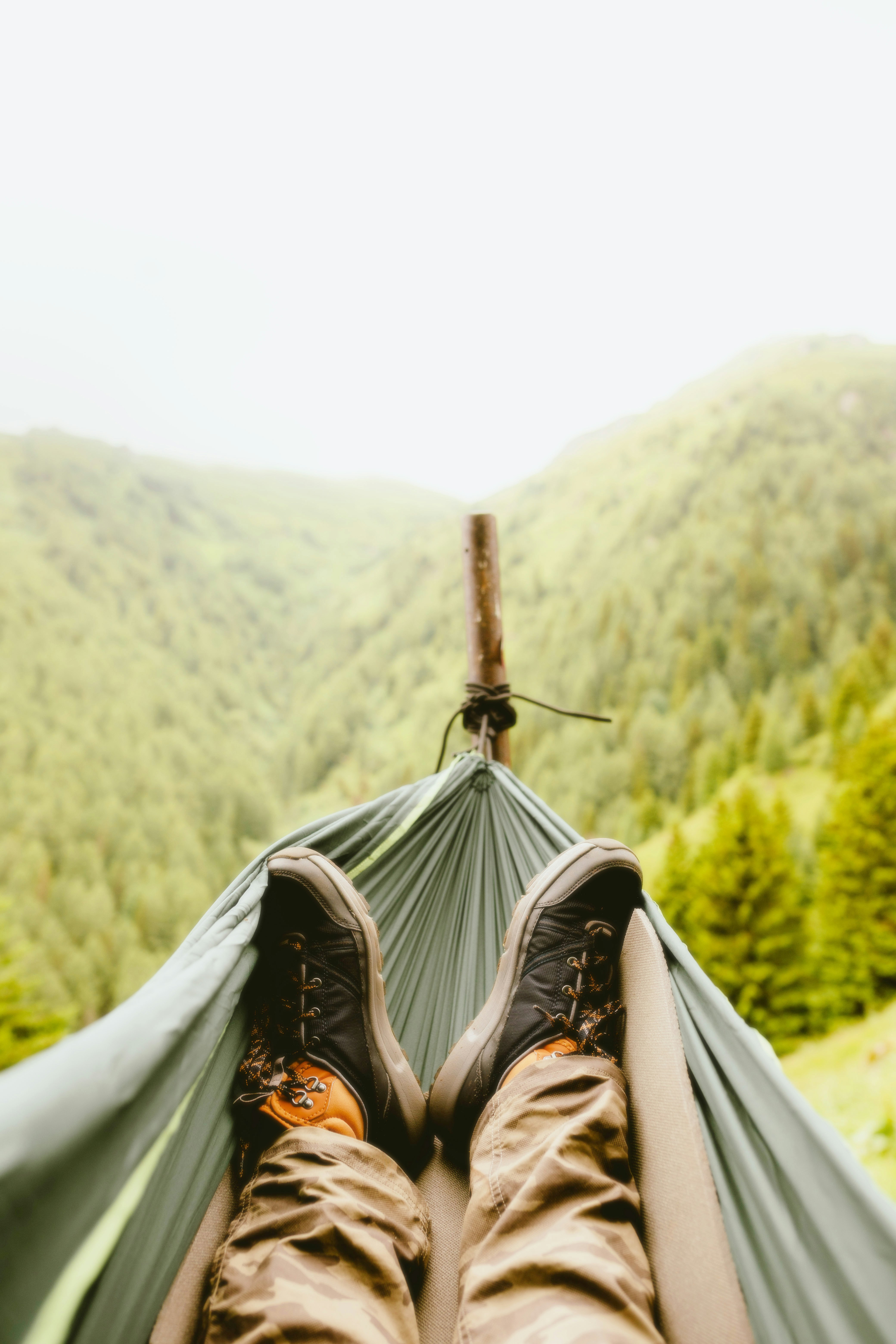 Person relaxing in a hammock overlooking lush green hills.