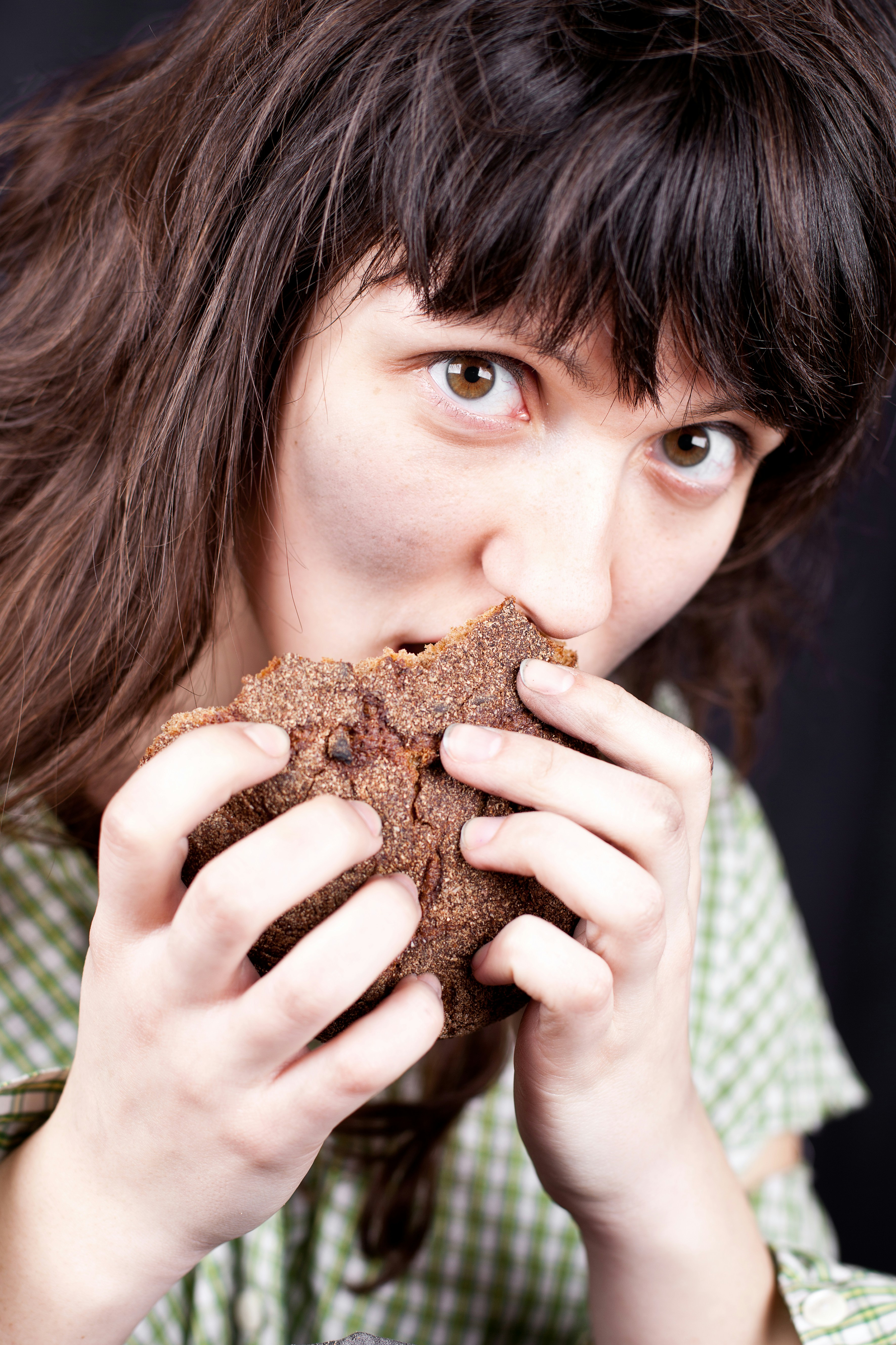Close-up of a girl tasting a chunk of brown bread, eyes drawing you in