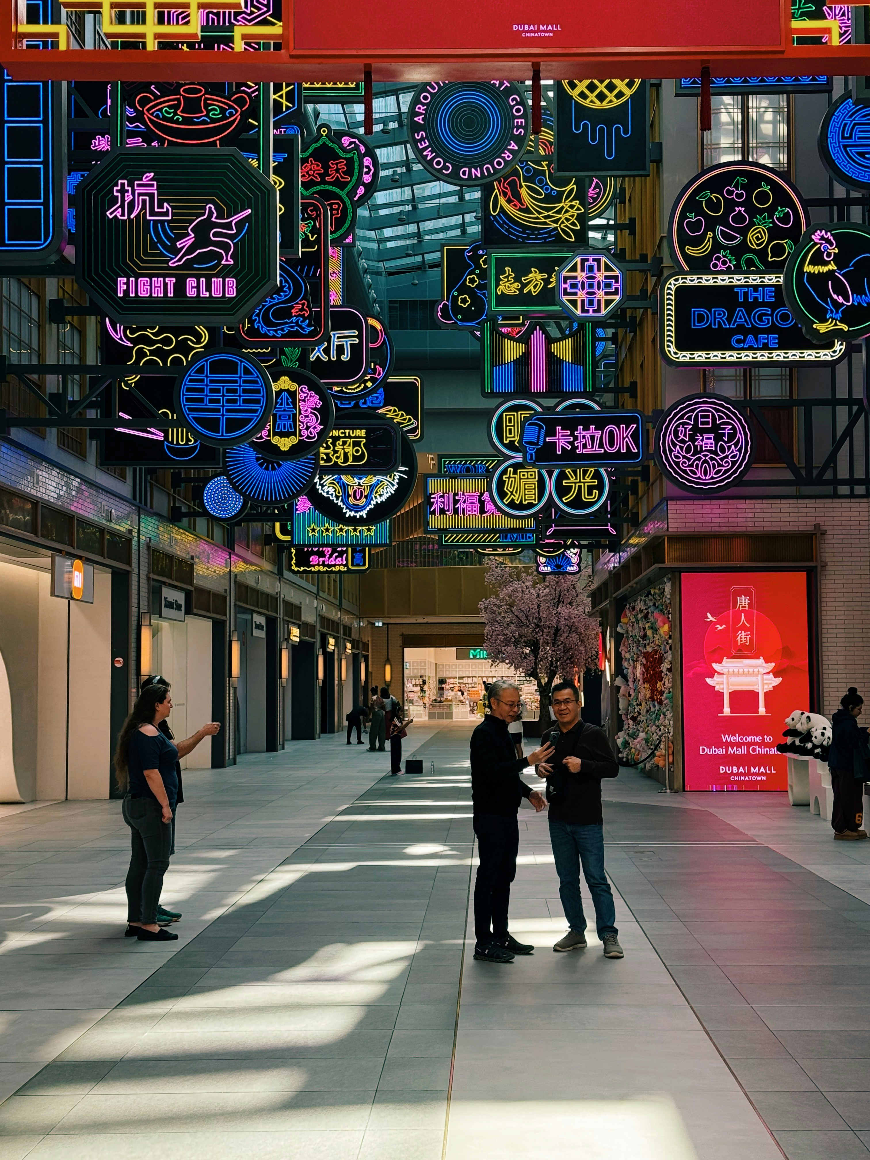 Two Friends Conversing Under a Tapestry of Neon Signs in Dubai Mall Atrium