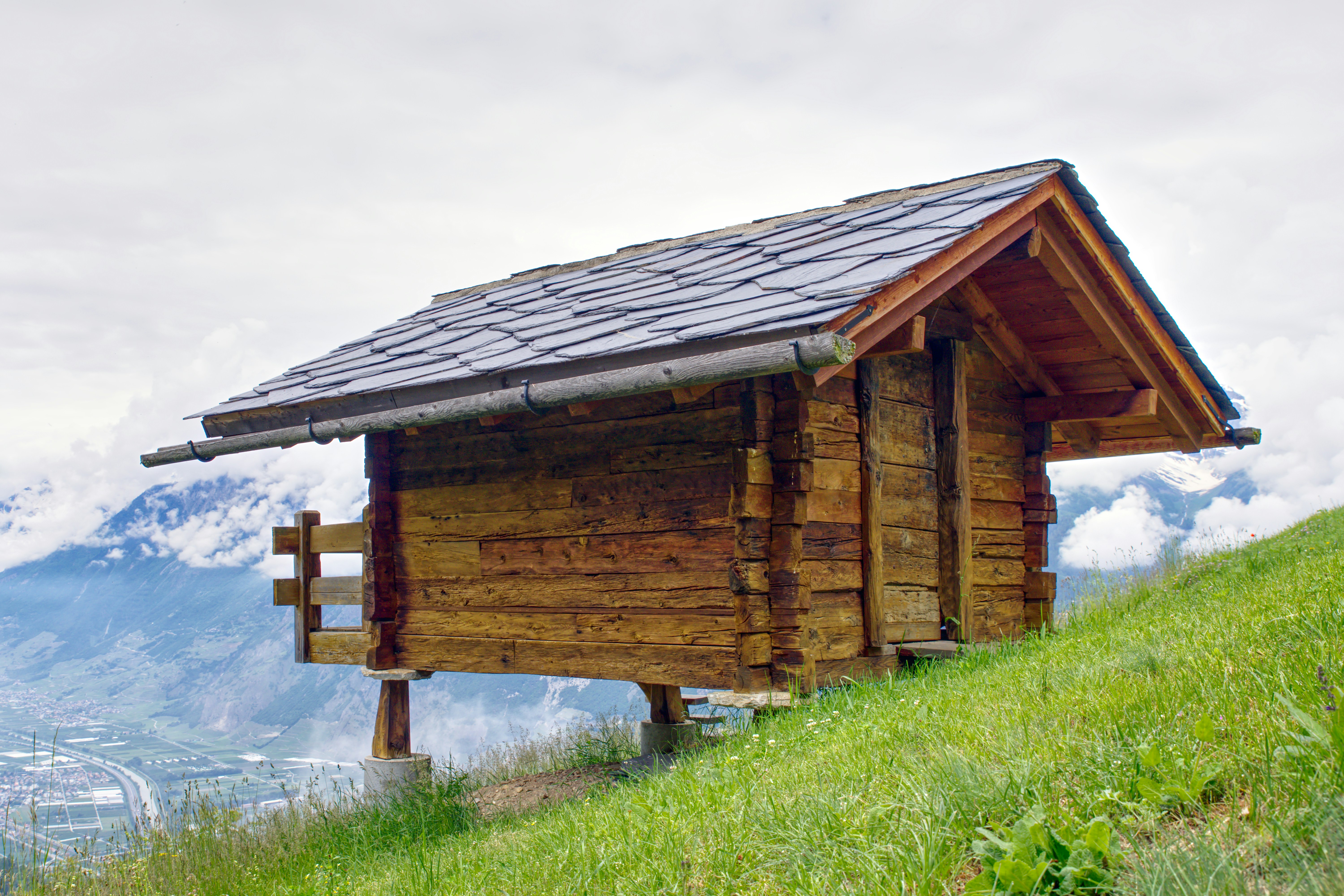 A wooden cabin on a grassy hill with mountains in the background photo ...