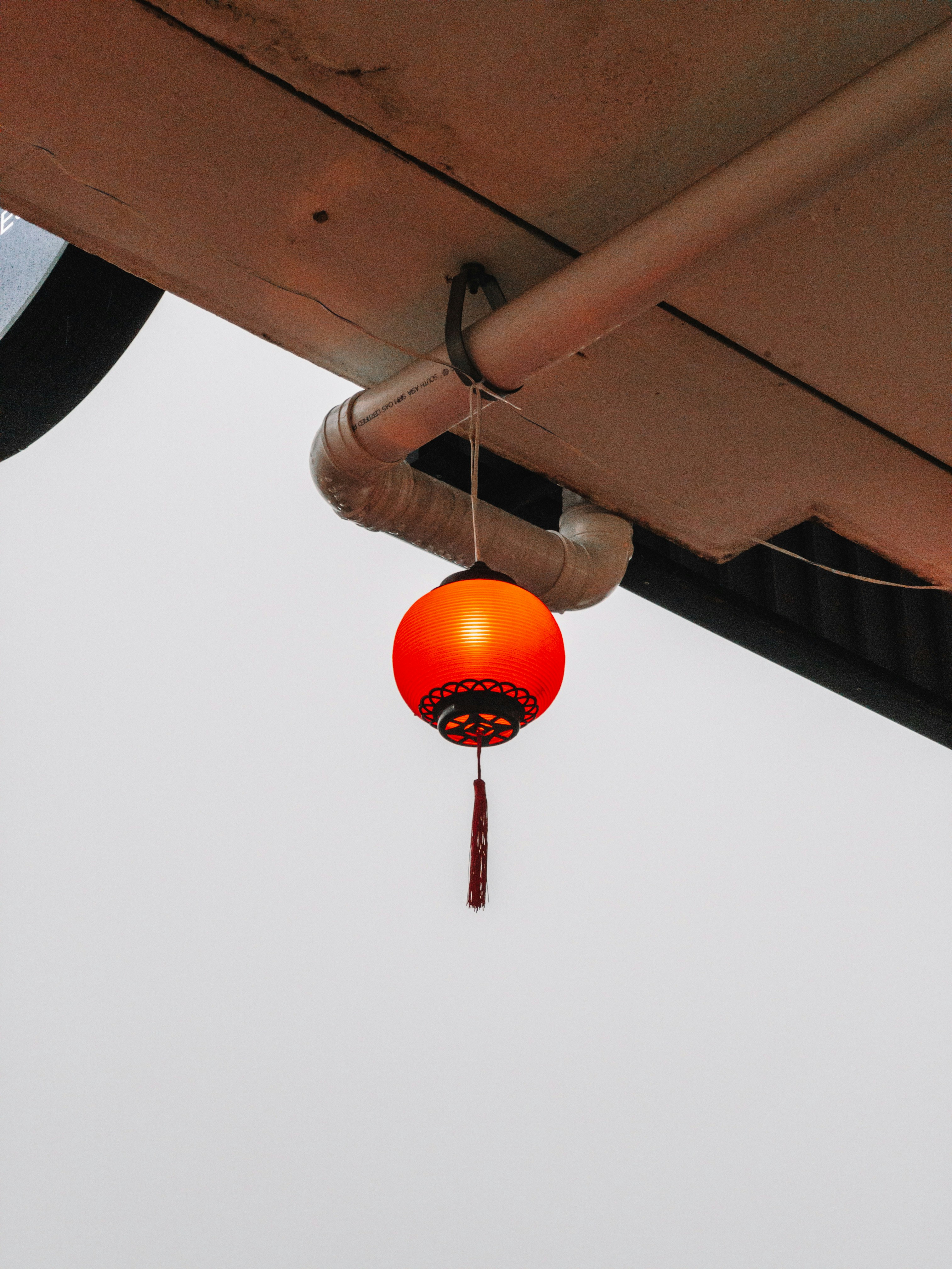 Crimson Lantern Dangling Beneath an Industrial Roofline