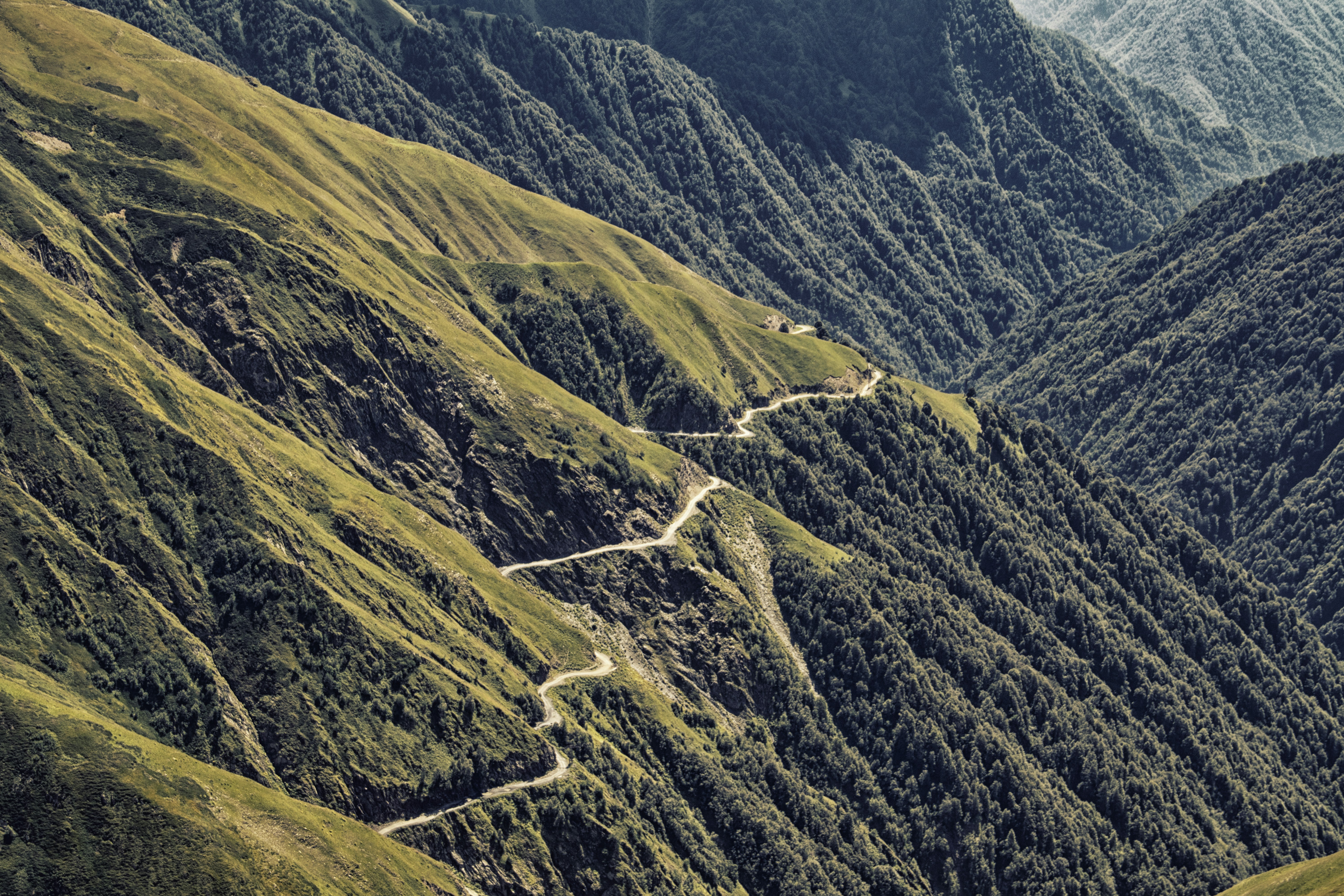 Winding mountain road cutting through lush green slopes under a clear sky.