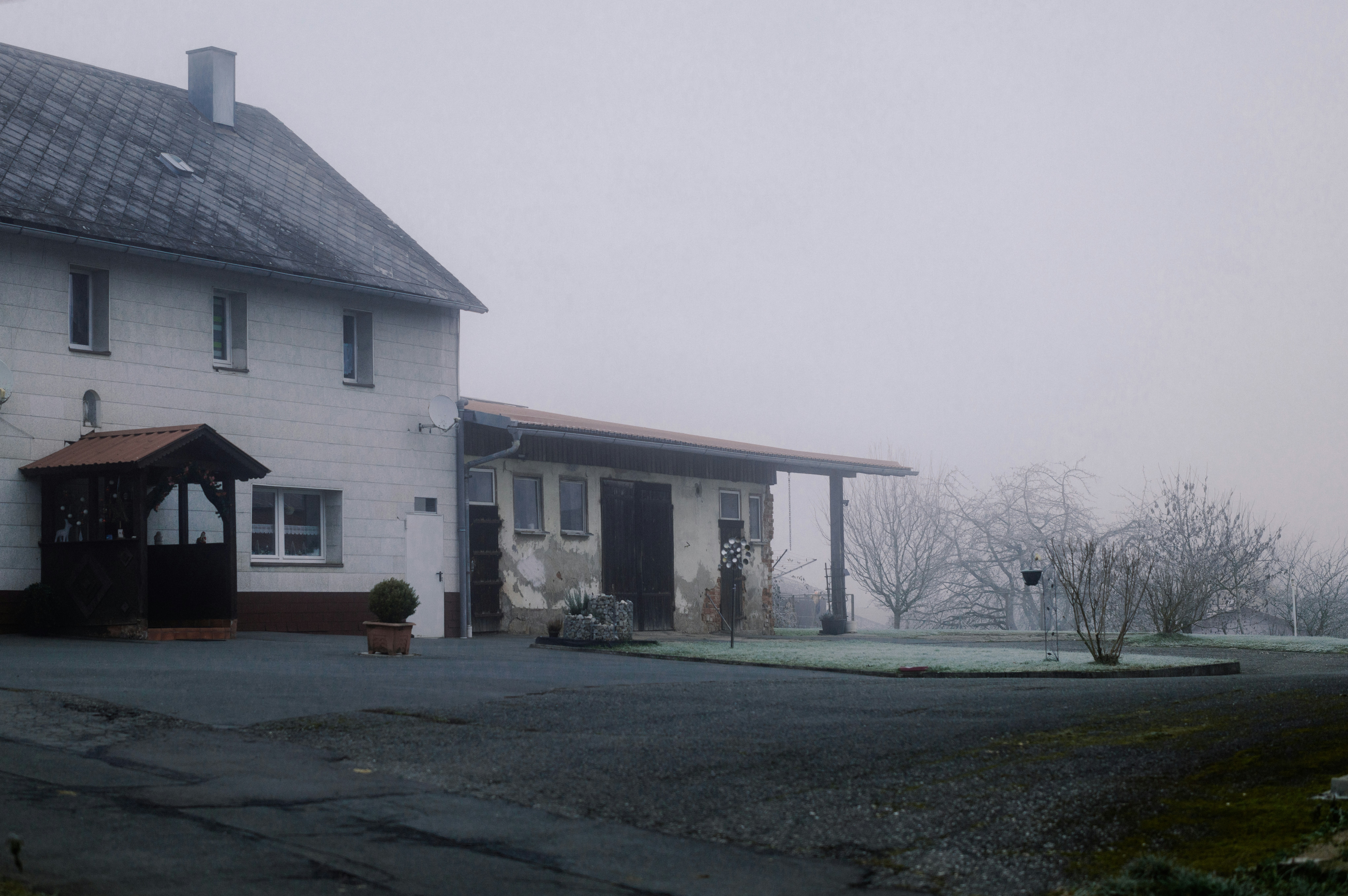 Rustic farmhouse enveloped in soft morning fog with bare trees in the background.