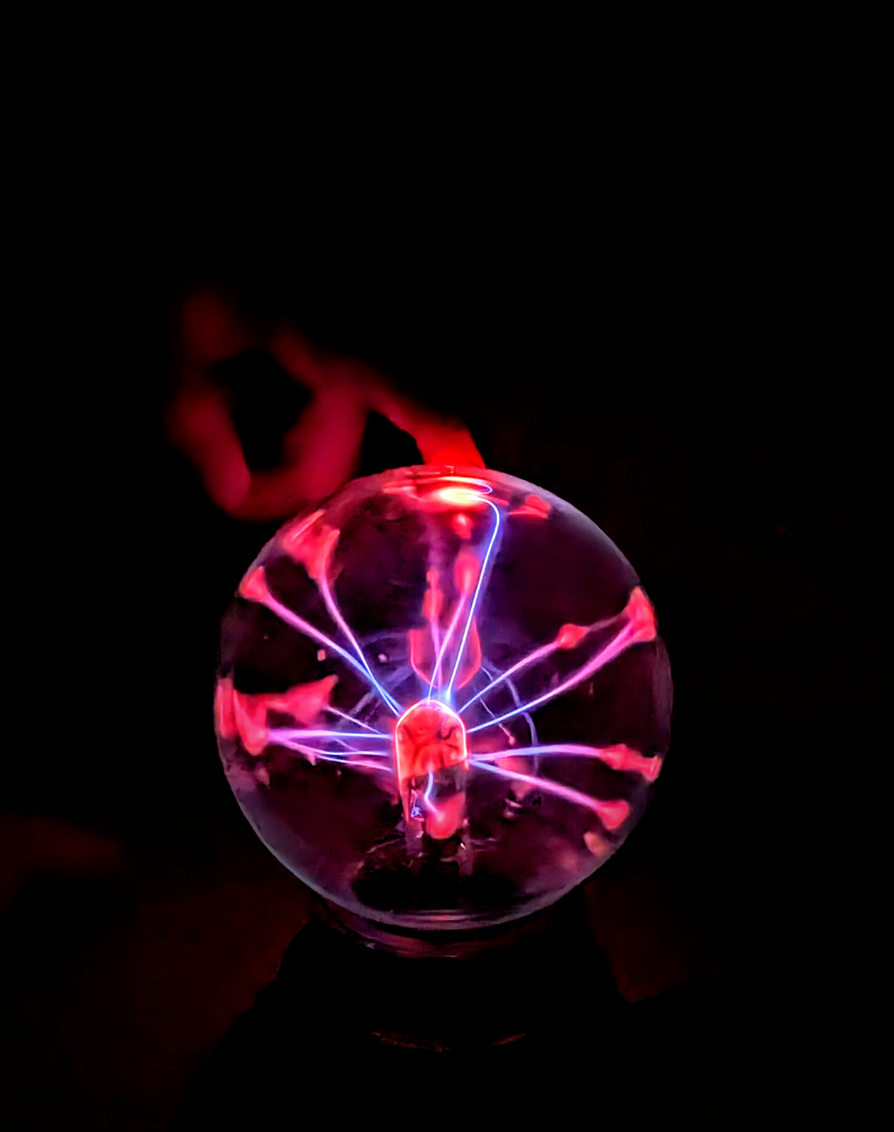Plasma globe with vibrant pink and blue electric arcs inside a dark room.