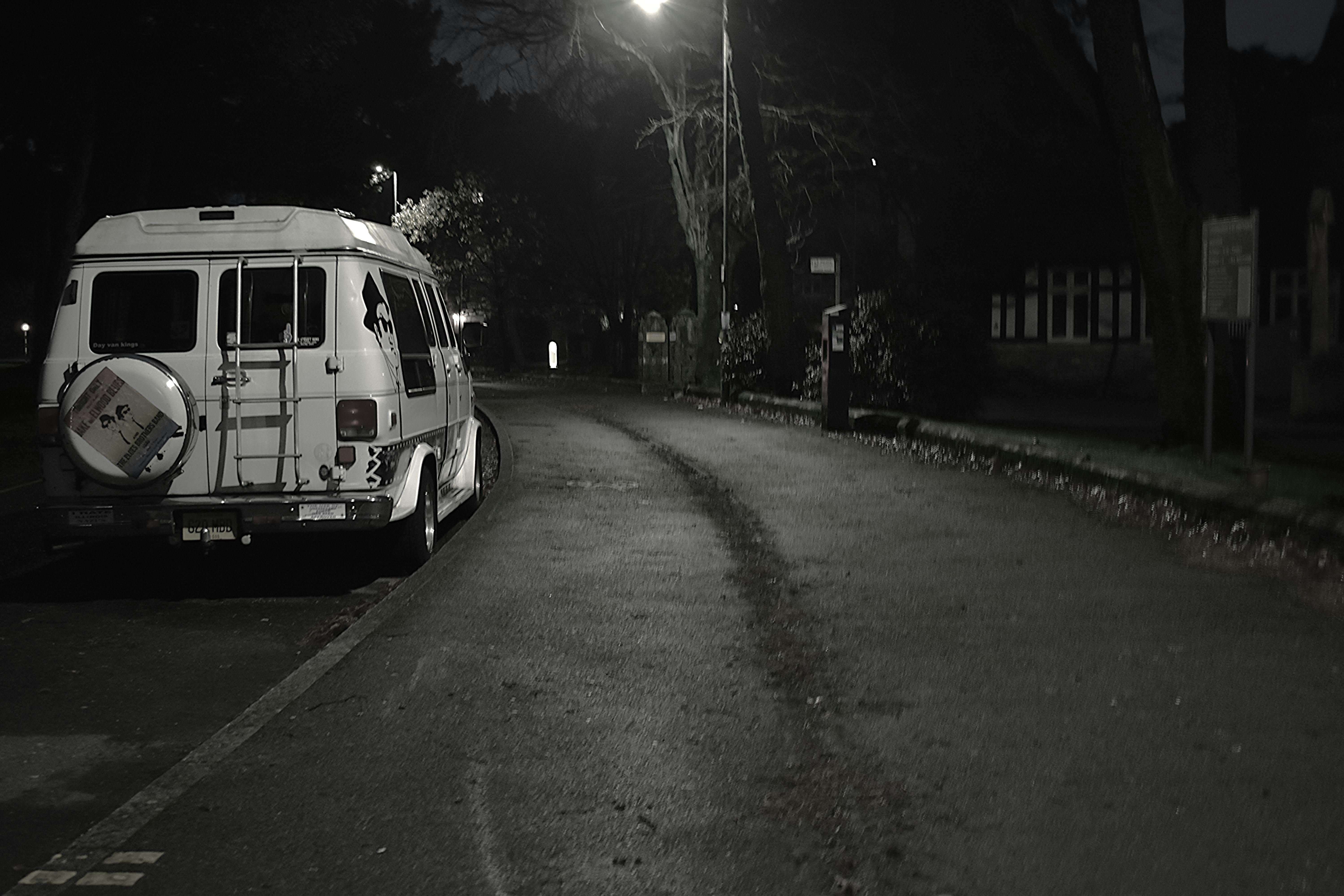White van parked on a deserted street illuminated by a single streetlamp at night.