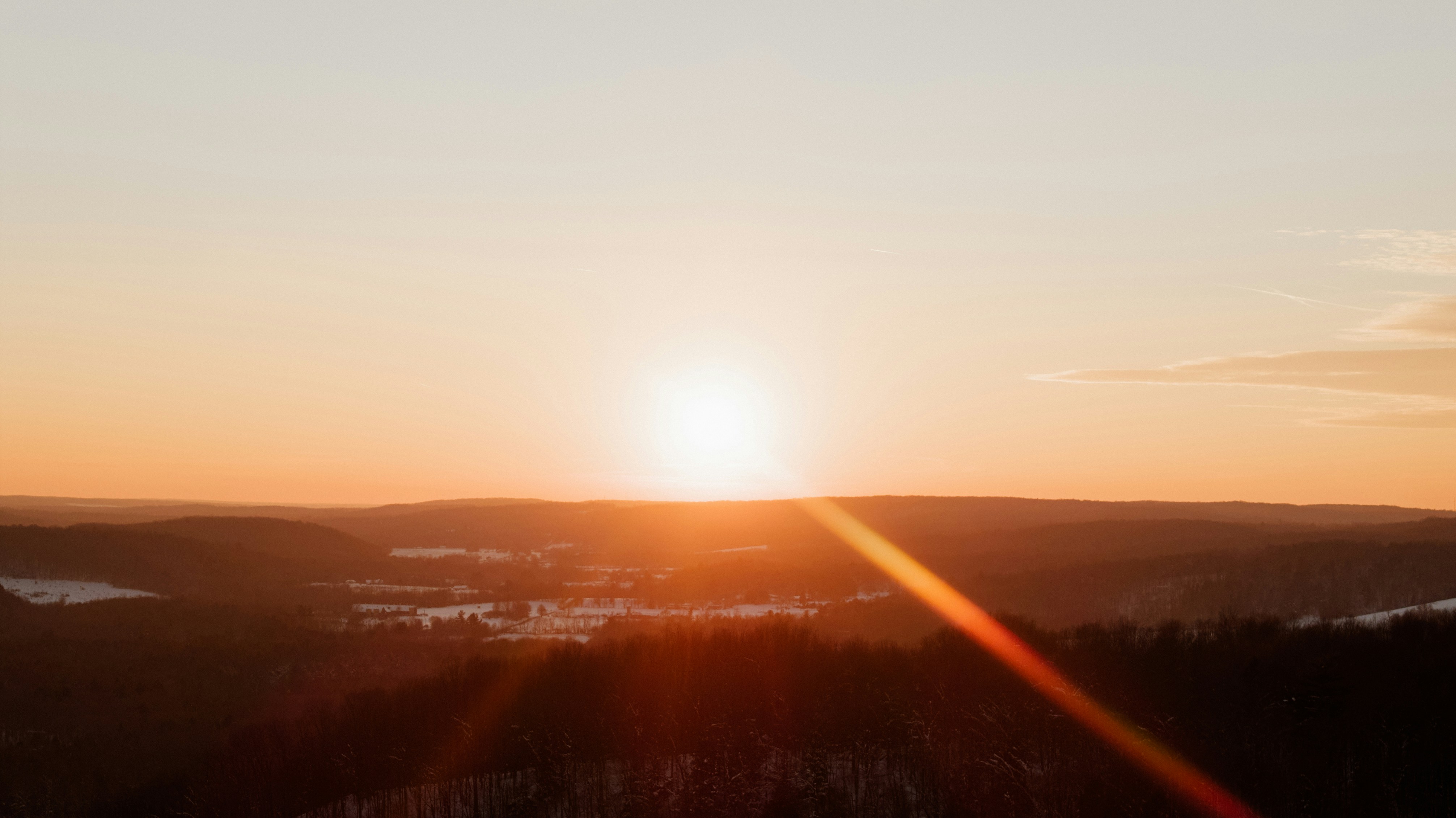 Sun setting over snow-dusted mountains with a warm glow.