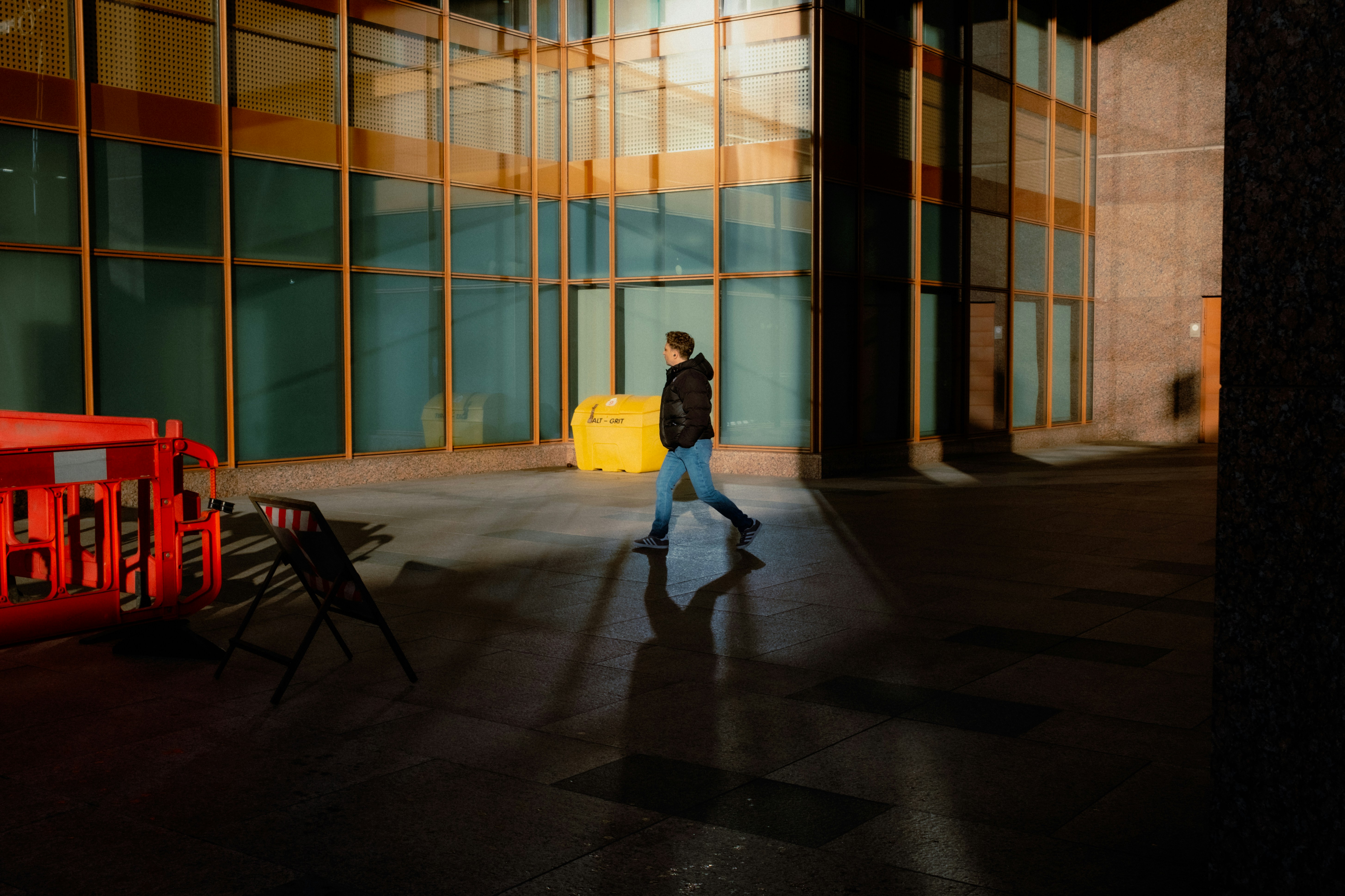 Person walking past glass building with dramatic shadows in Canary Wharf.