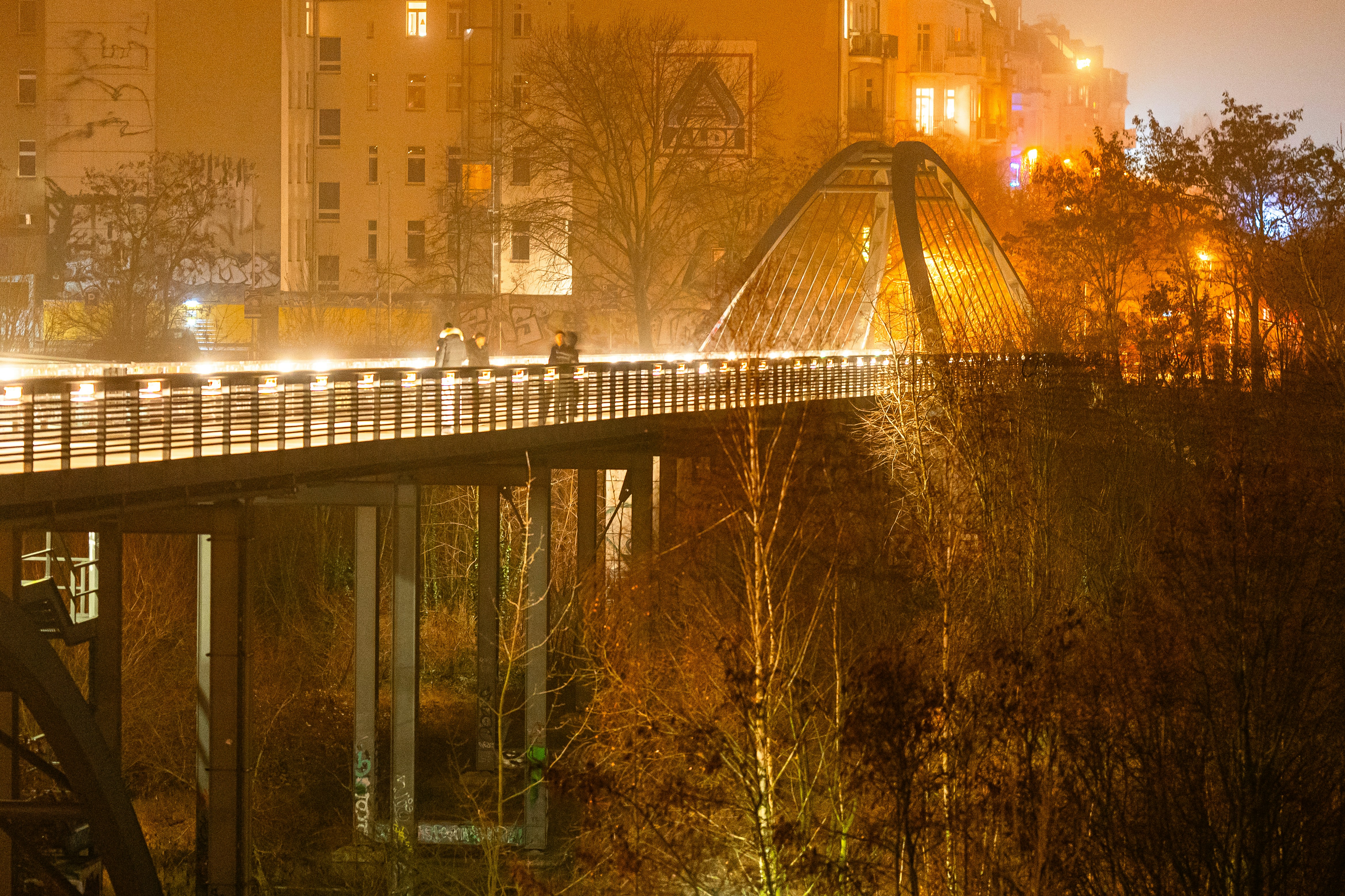 Arc of Light over the Amber Bridge: Night Walkers Beneath a Warm City Glow