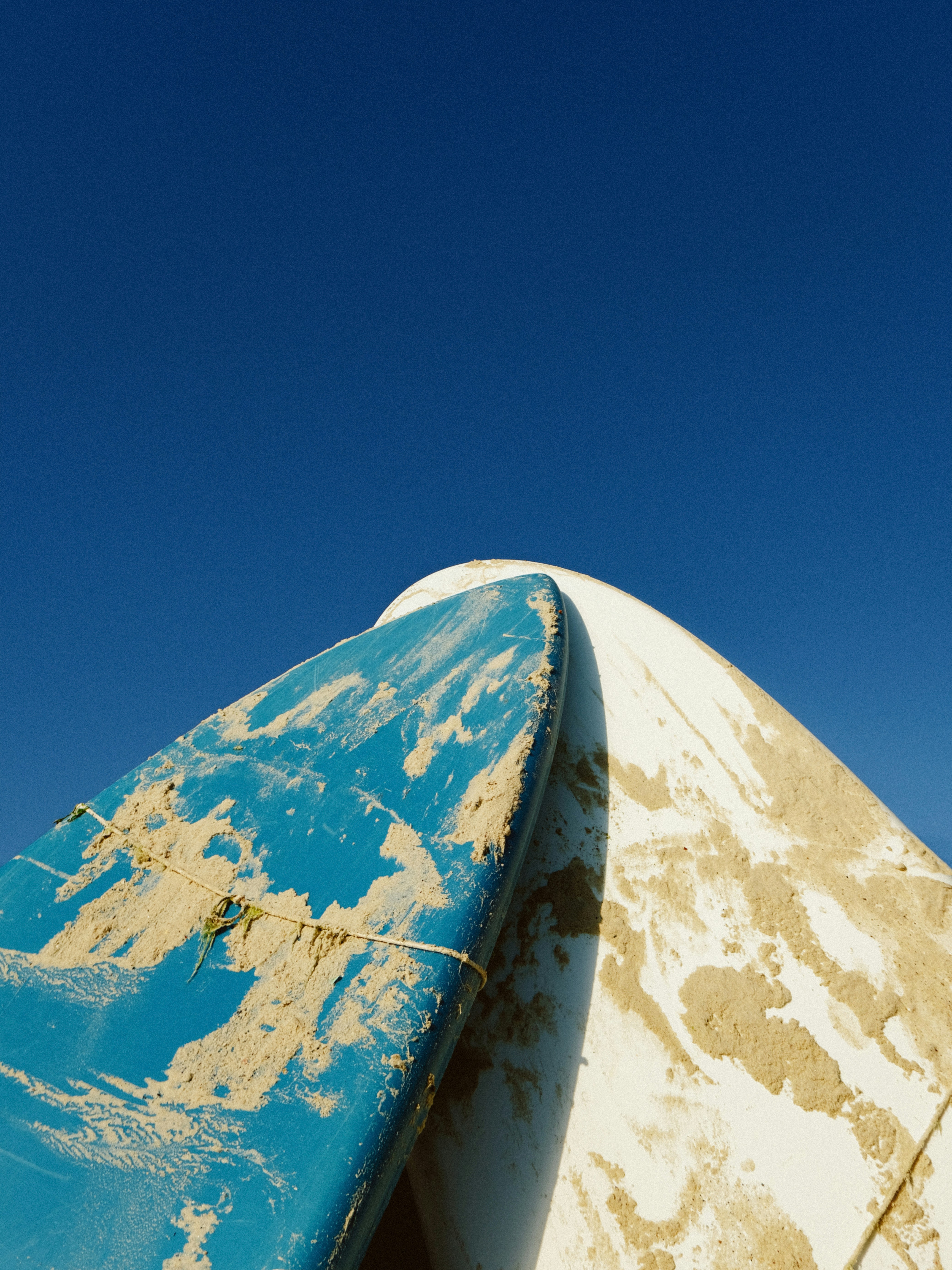 Two Weathered Surfboards Lean Into a Pristine Blue Sky