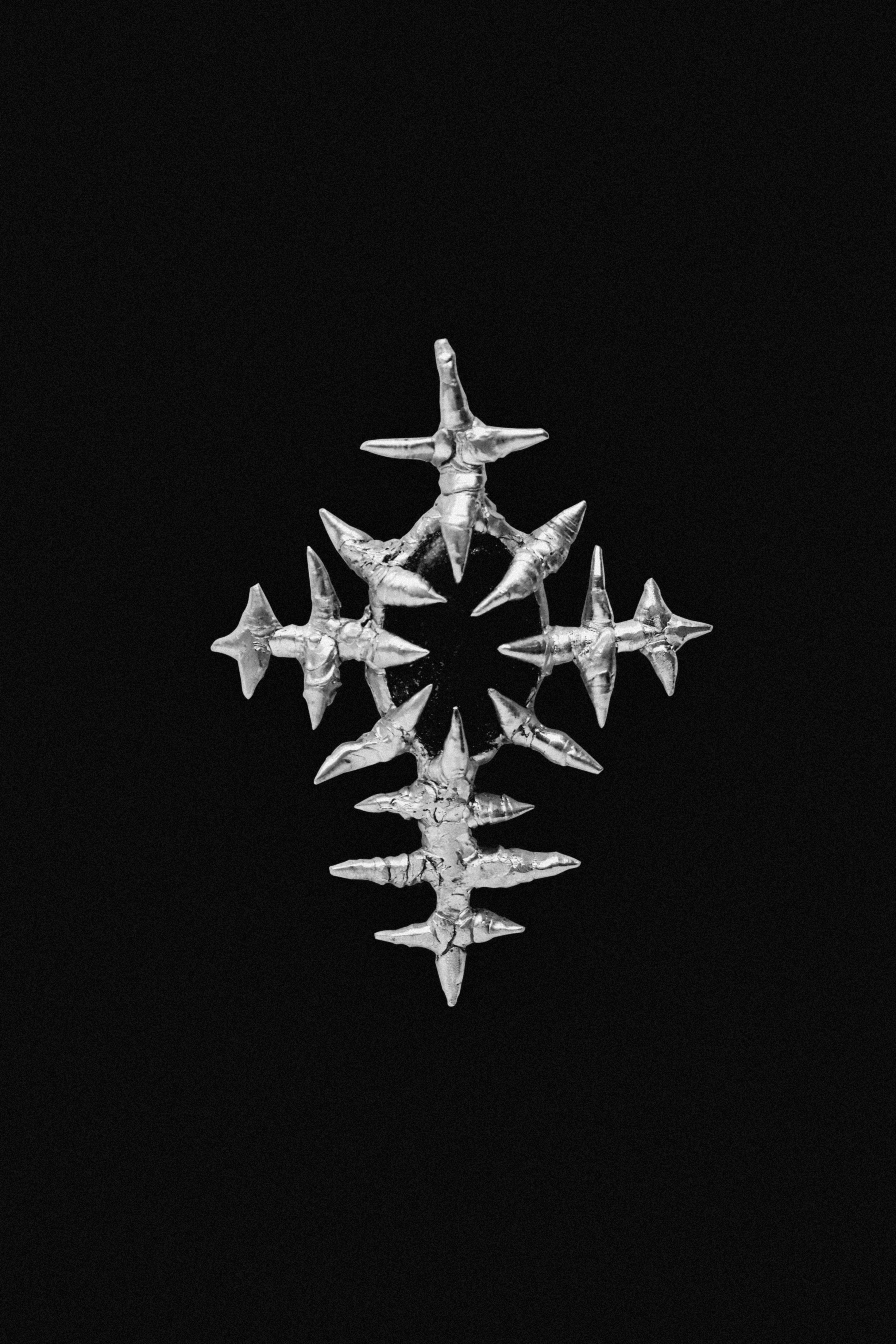 A striking metallic cross composed of sharp, star-like forms against a deep black background.