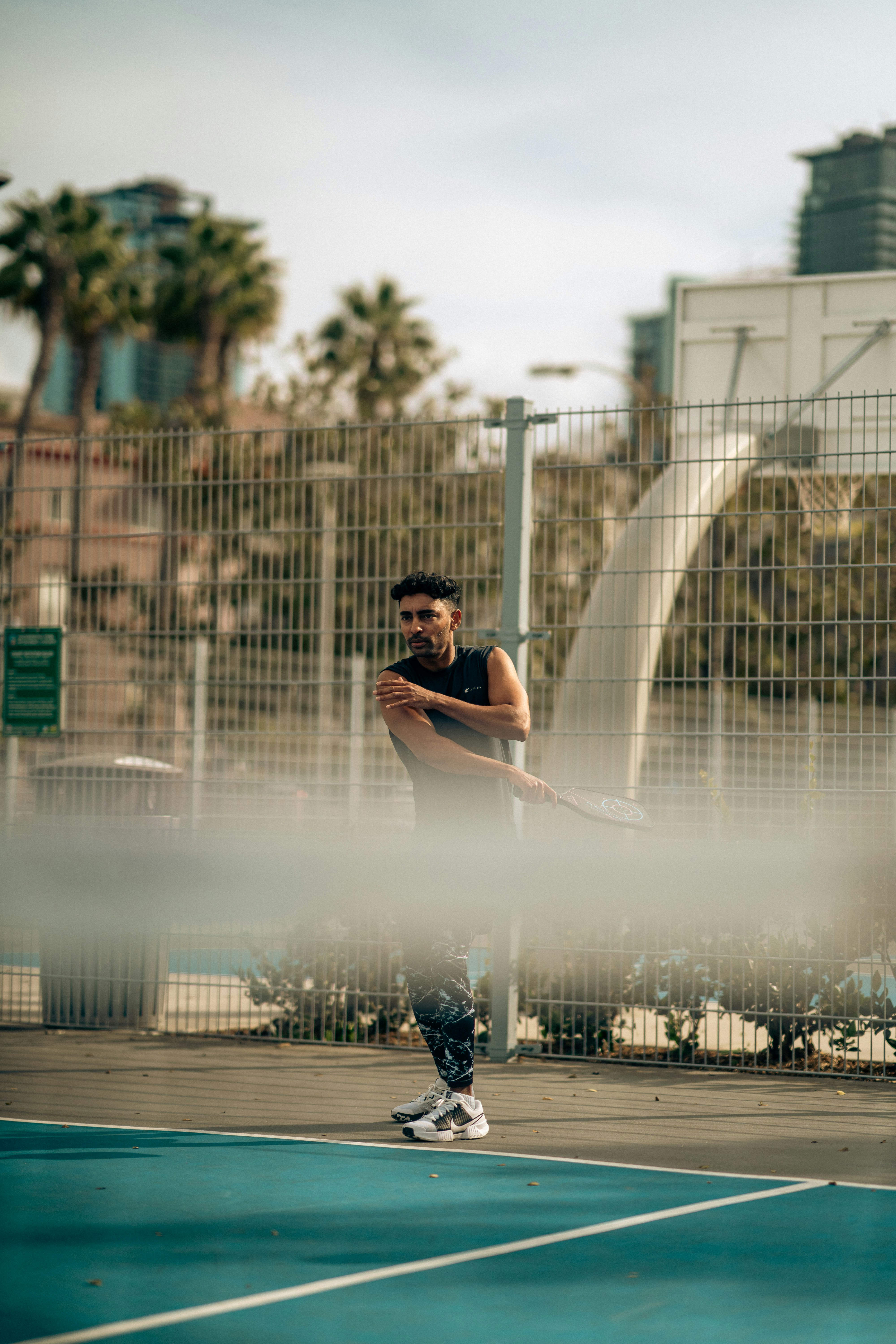 Blue Court Moment: A lone athlete paused in mid-stretch behind a city fence