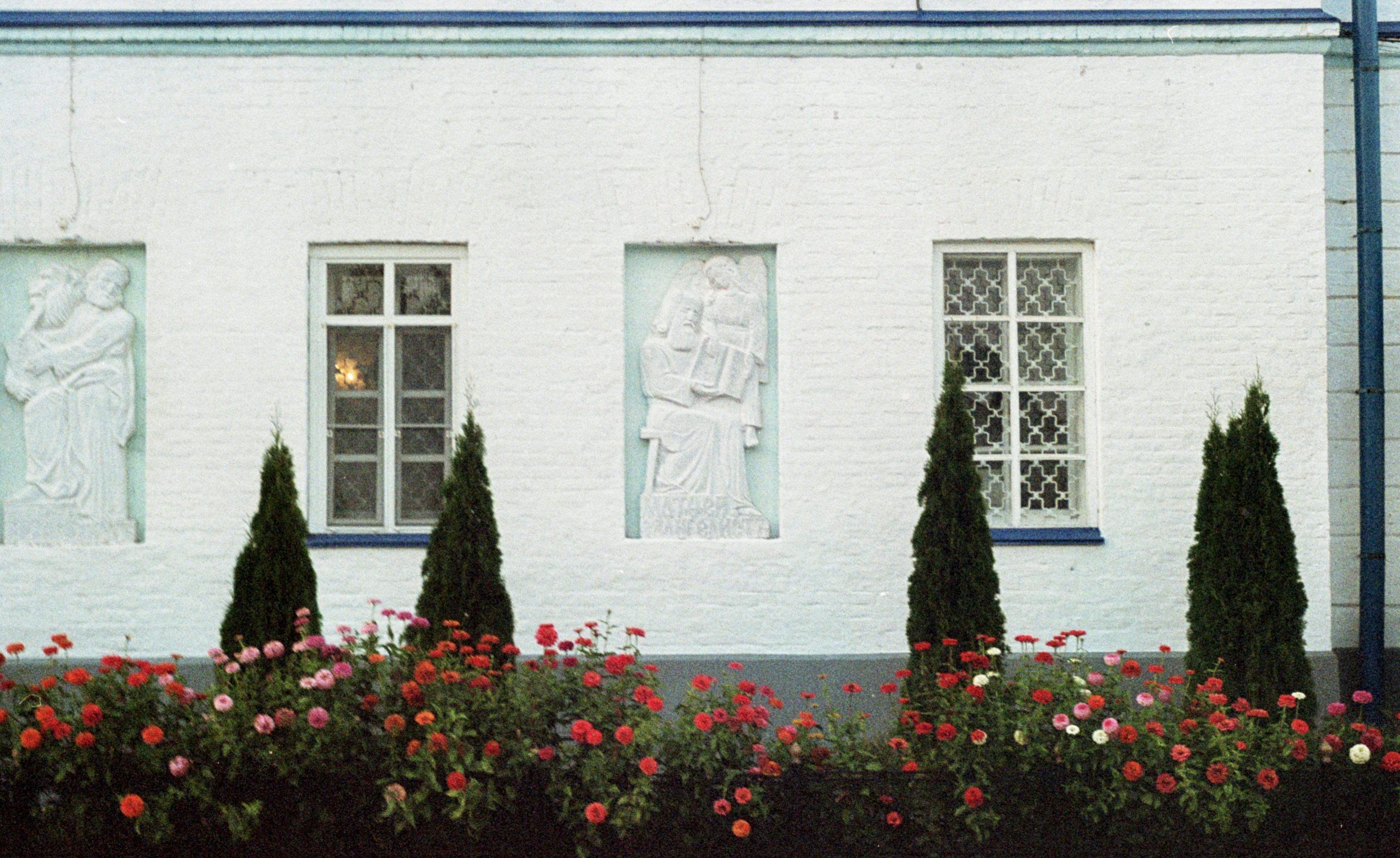 Colorful flower border along a white wall with sculpted reliefs and windows as the backdrop.