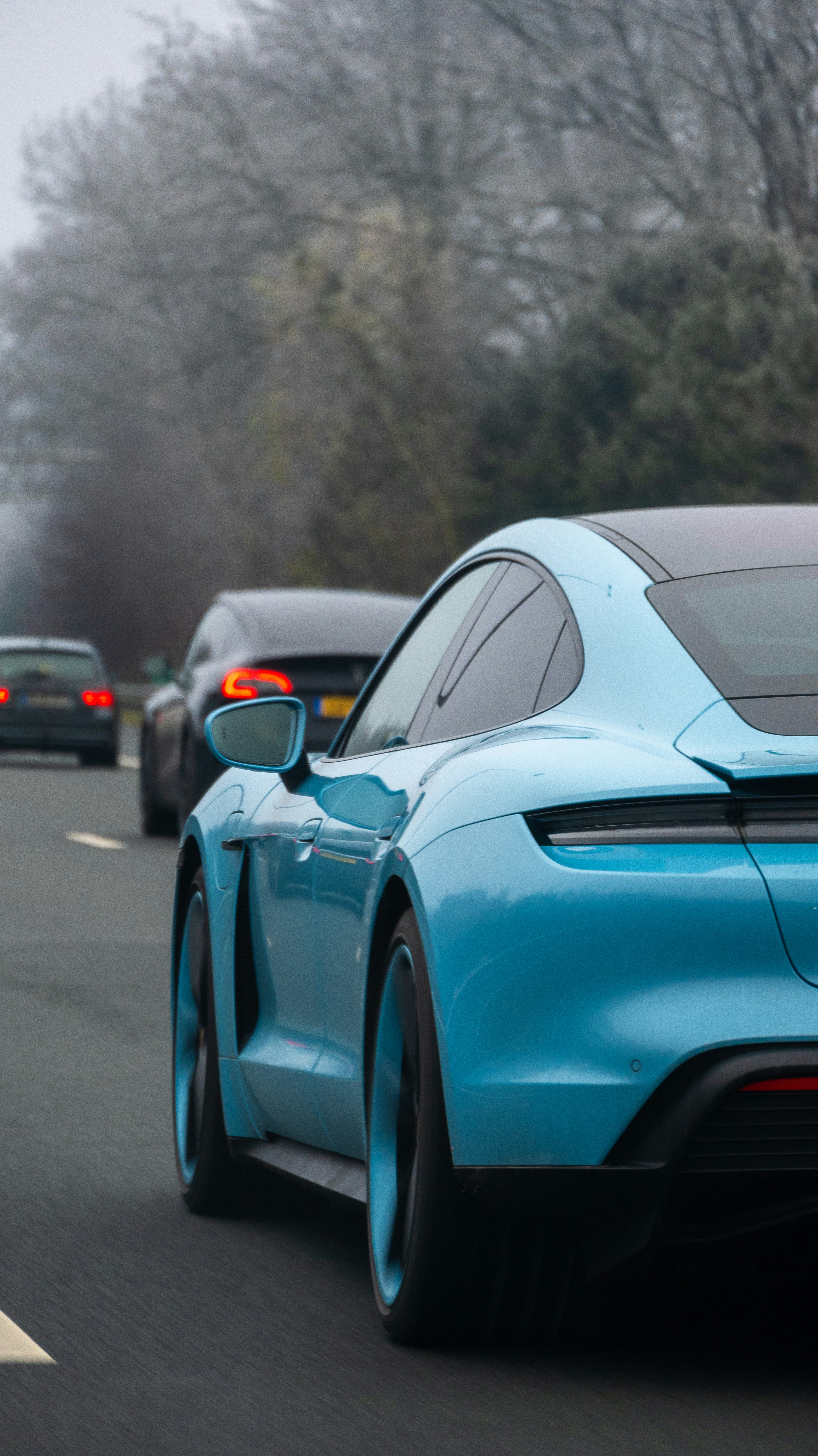 Blue sports car cruising on a misty highway with trees in the background.