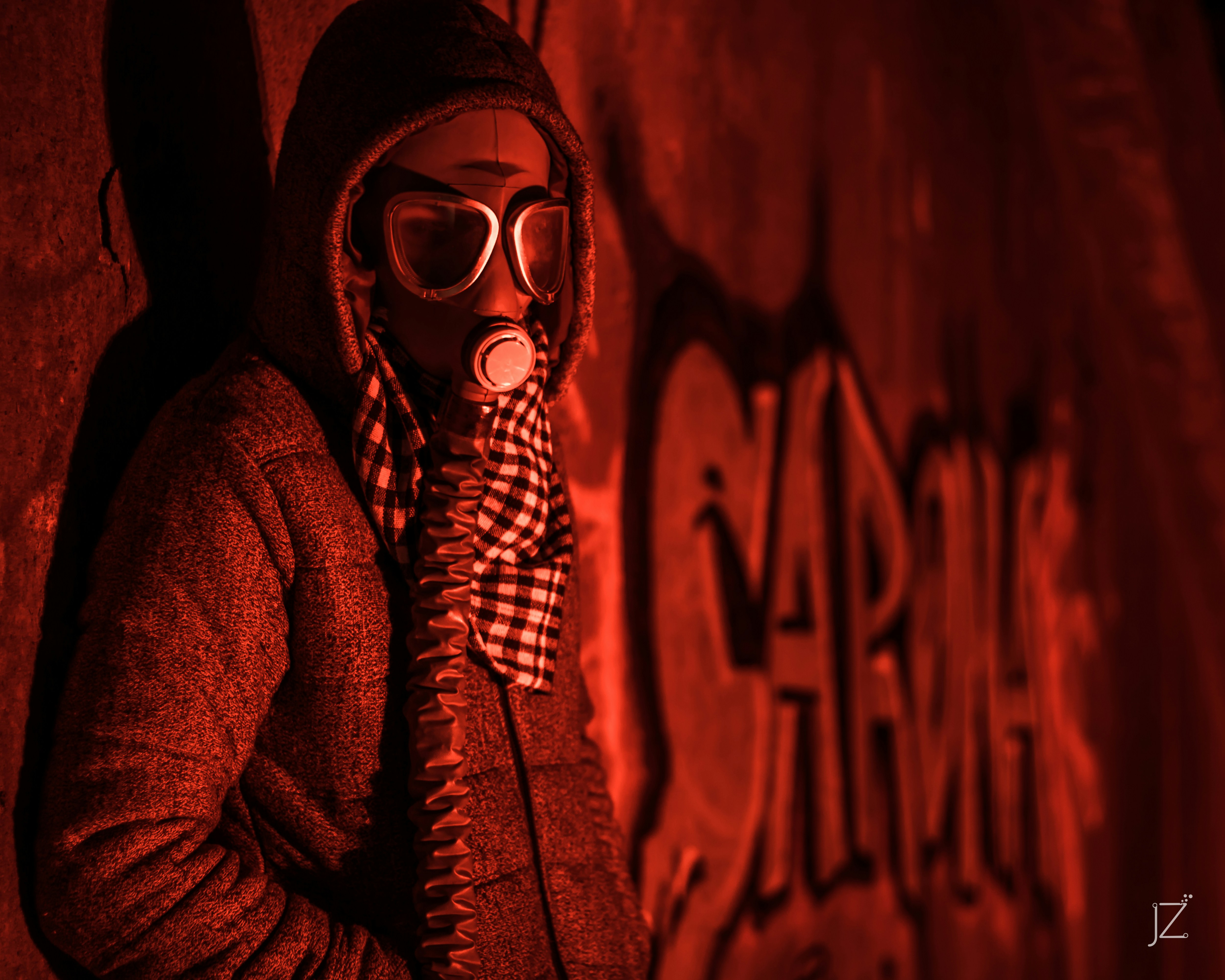A figure in a gas mask leans against a graffiti-covered wall, illuminated by a warm red light that enhances the urban atmosphere.