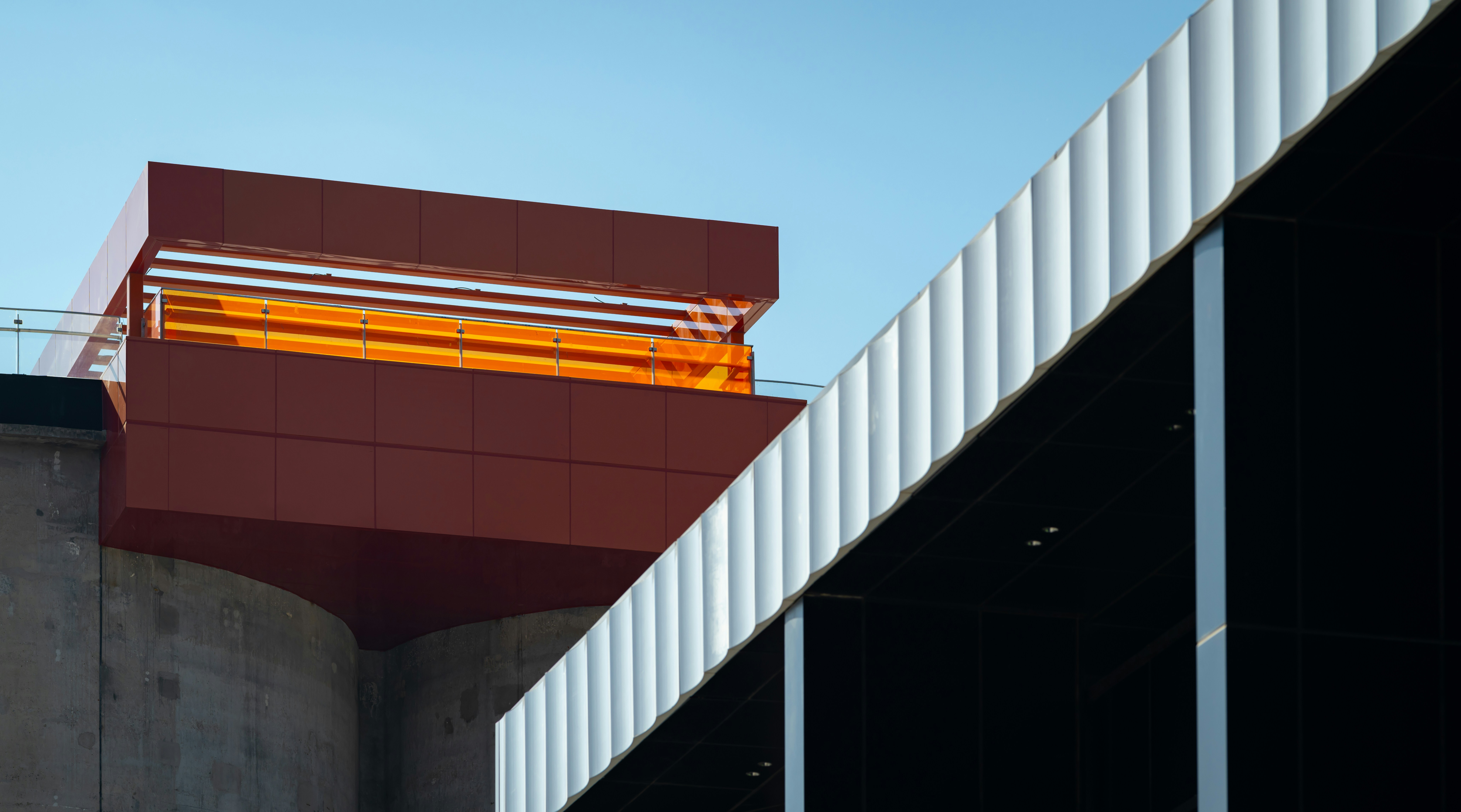 Cantilevered Orange Prism Over a Concrete Pillar Against a Clear Sky