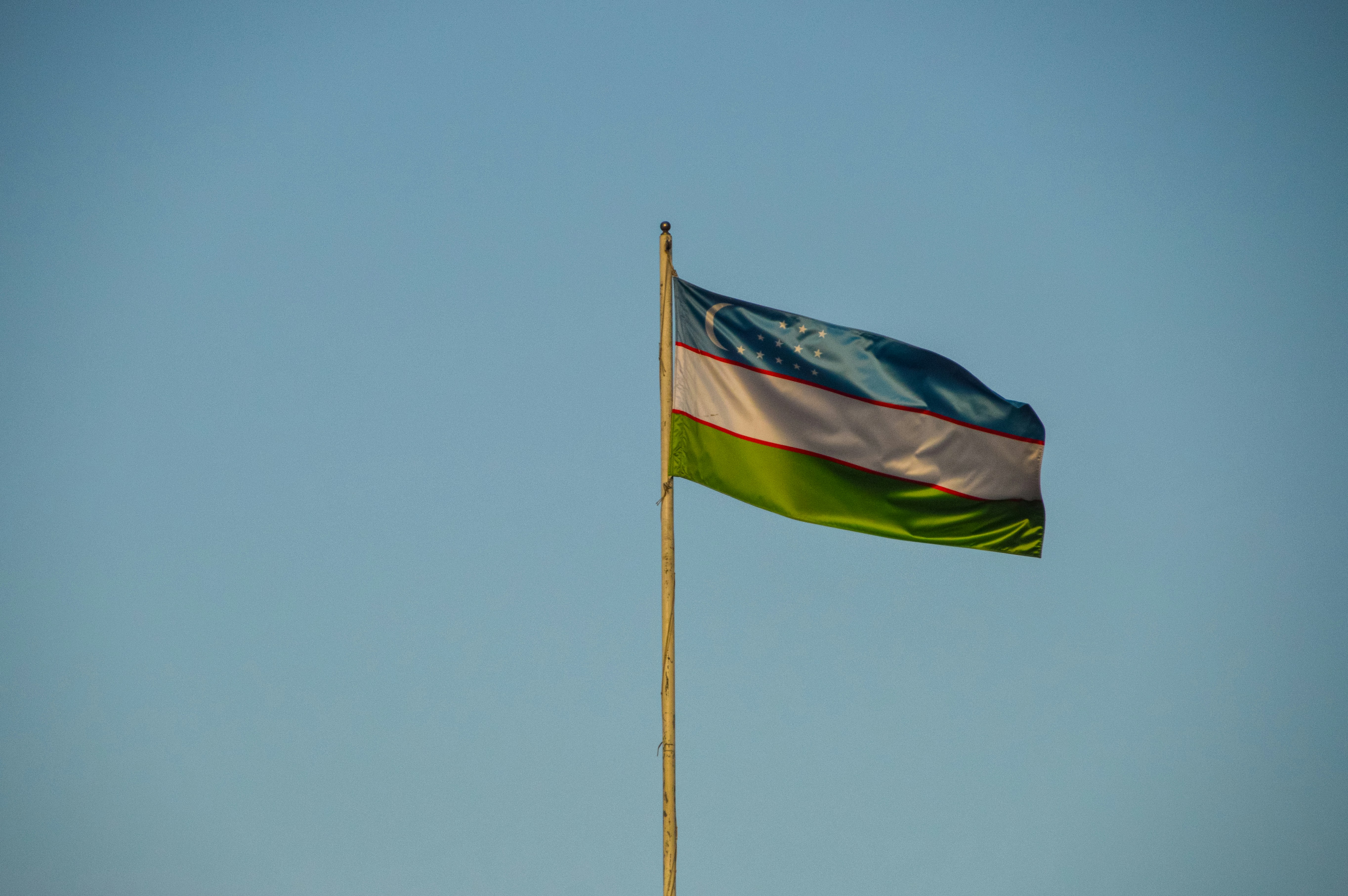 Uzbekistan's national flag fluttering against a clear blue sky, showcasing its vibrant colors and emblematic design.