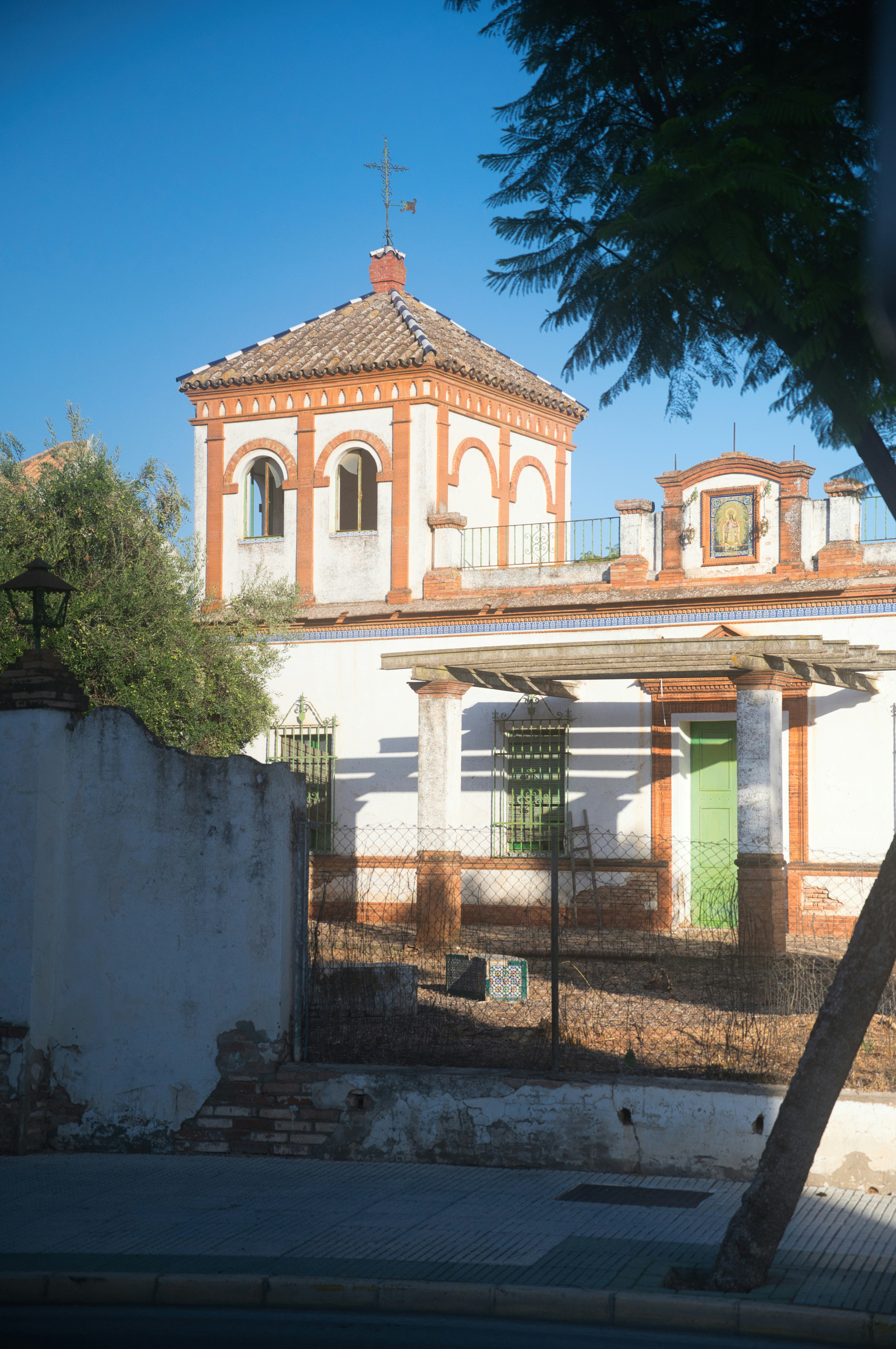 Historic building featuring a distinctive tiled roof and vibrant green doors, framed by lush greenery and weathered walls.