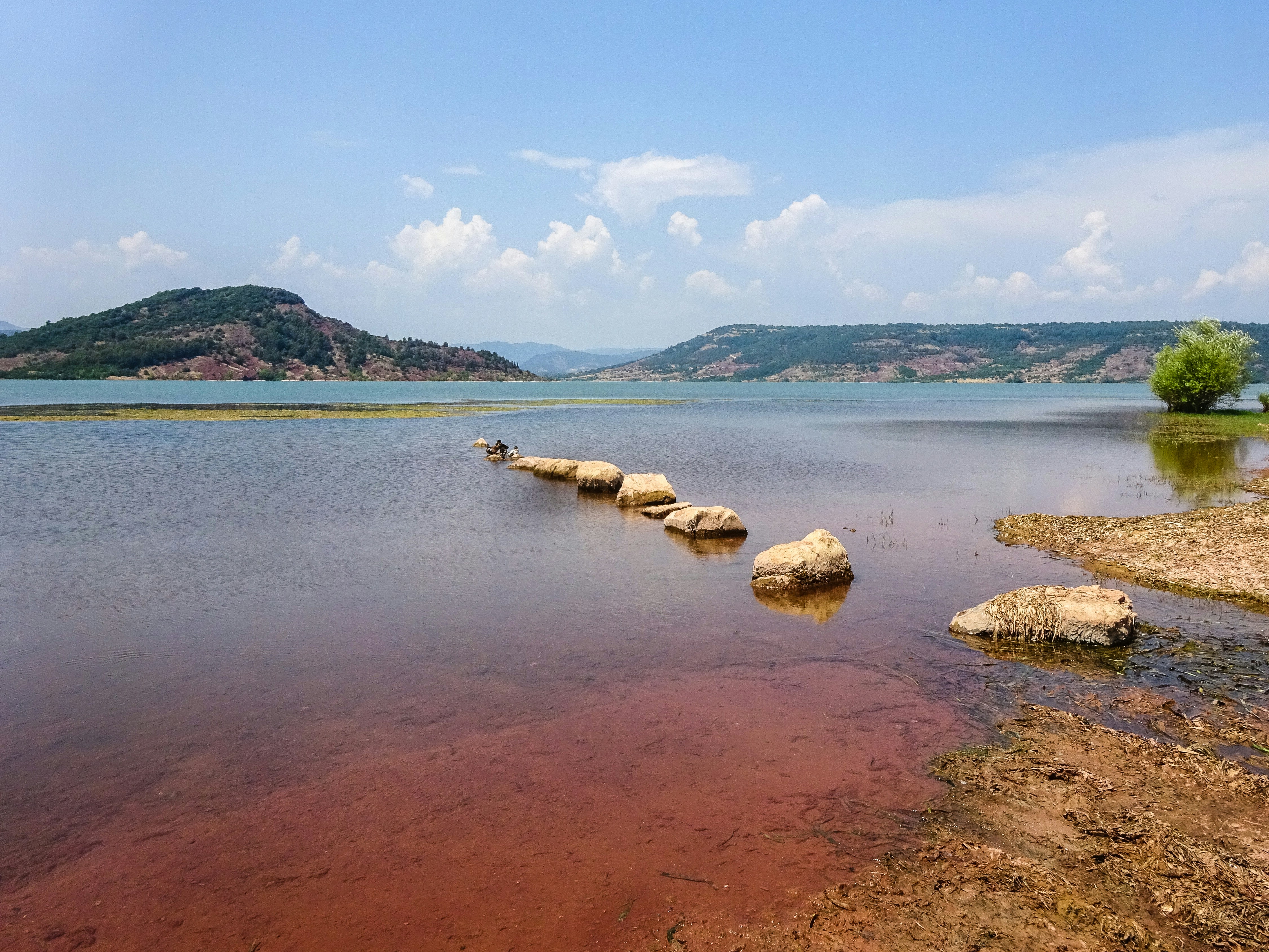 Row of stones leading across a calm lake with distant hills under a partly cloudy sky.