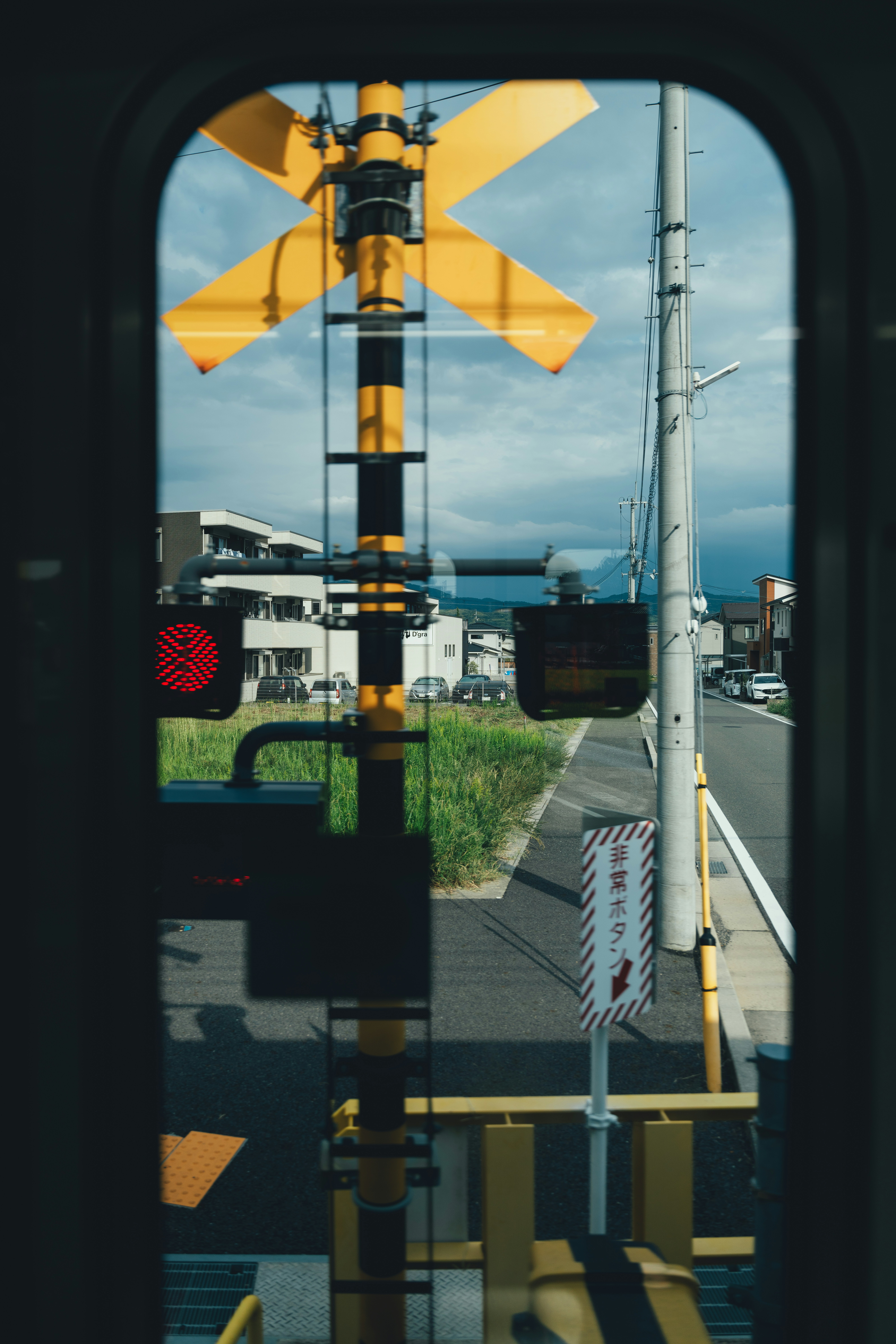 Through the Window: Suburban railway crossing with a bold yellow crossbuck under a blue sky
