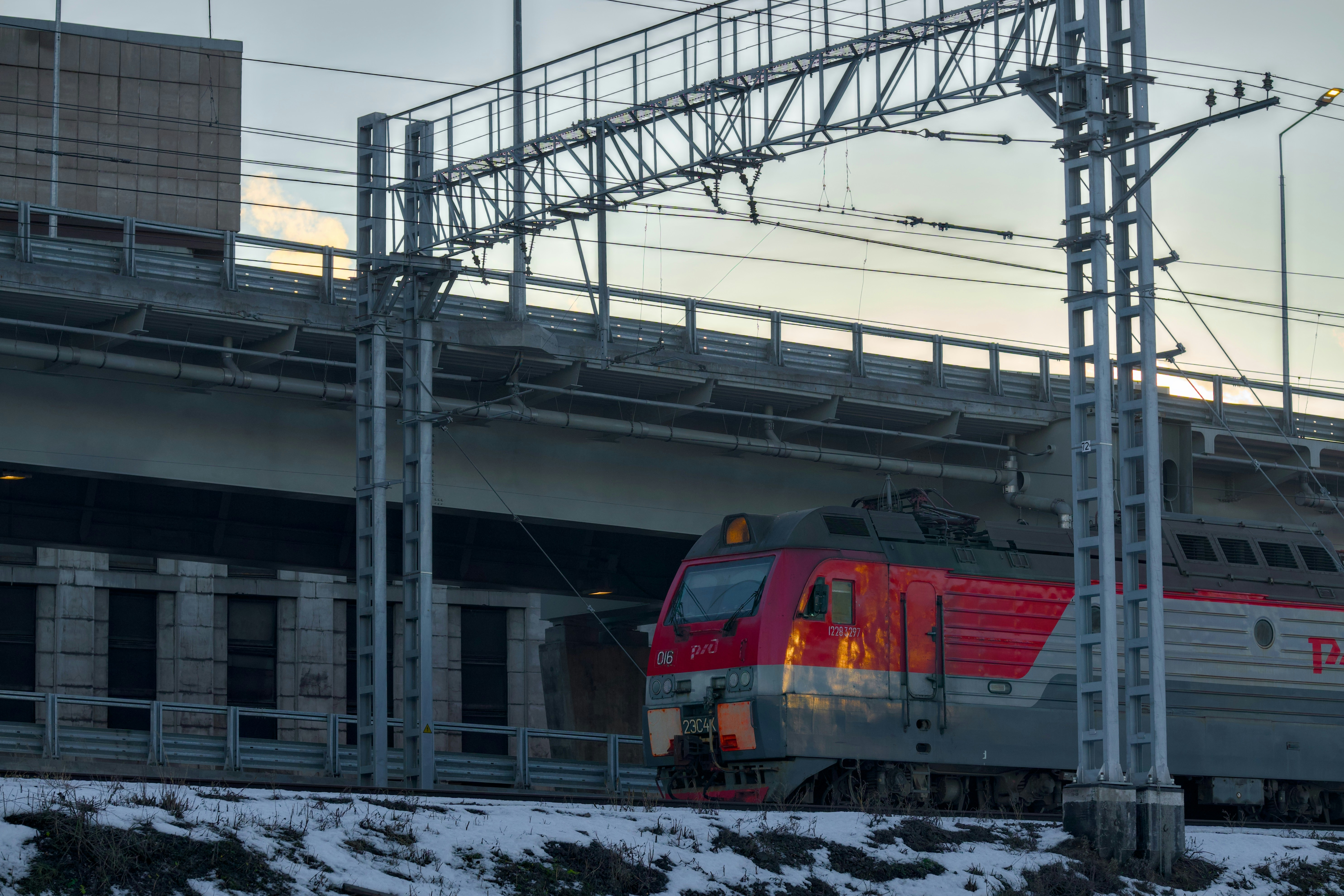 A red train traveling down train tracks next to a building photo – Free ...