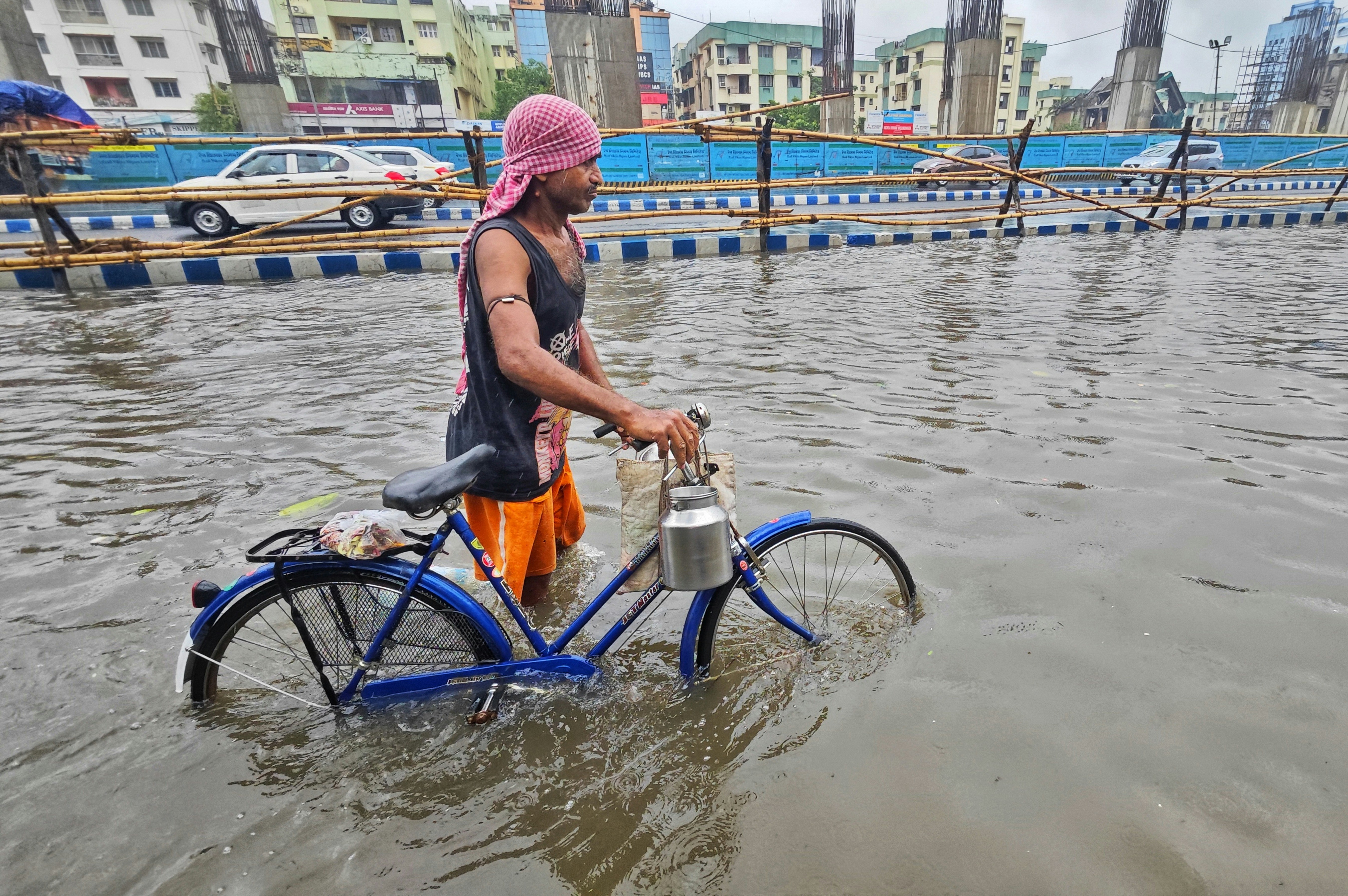 Man pushes a bicycle through a flooded street in a city setting.