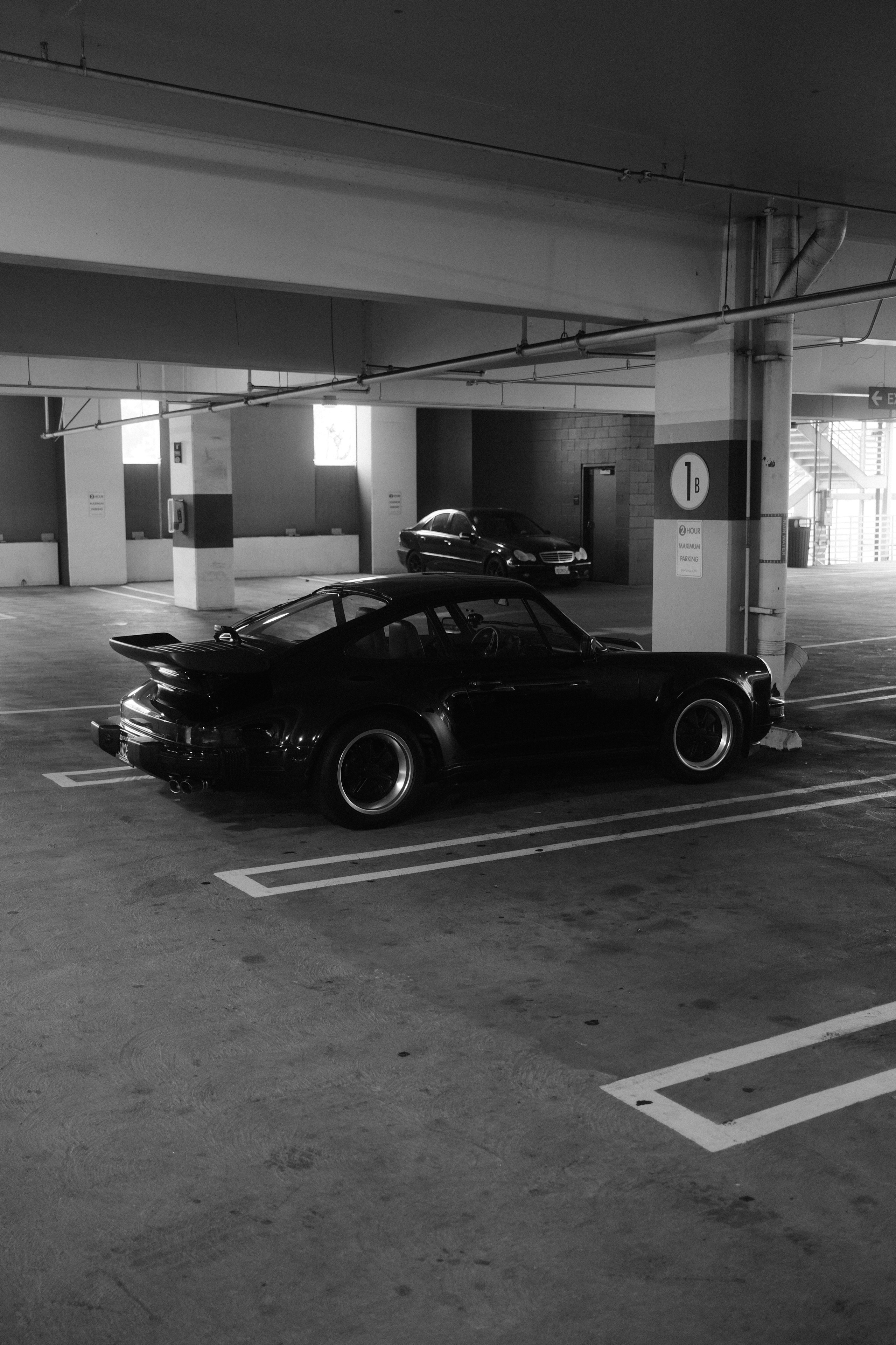 Noir Parking: A Black Porsche Resting Under Concrete Beams in a Dim Garage