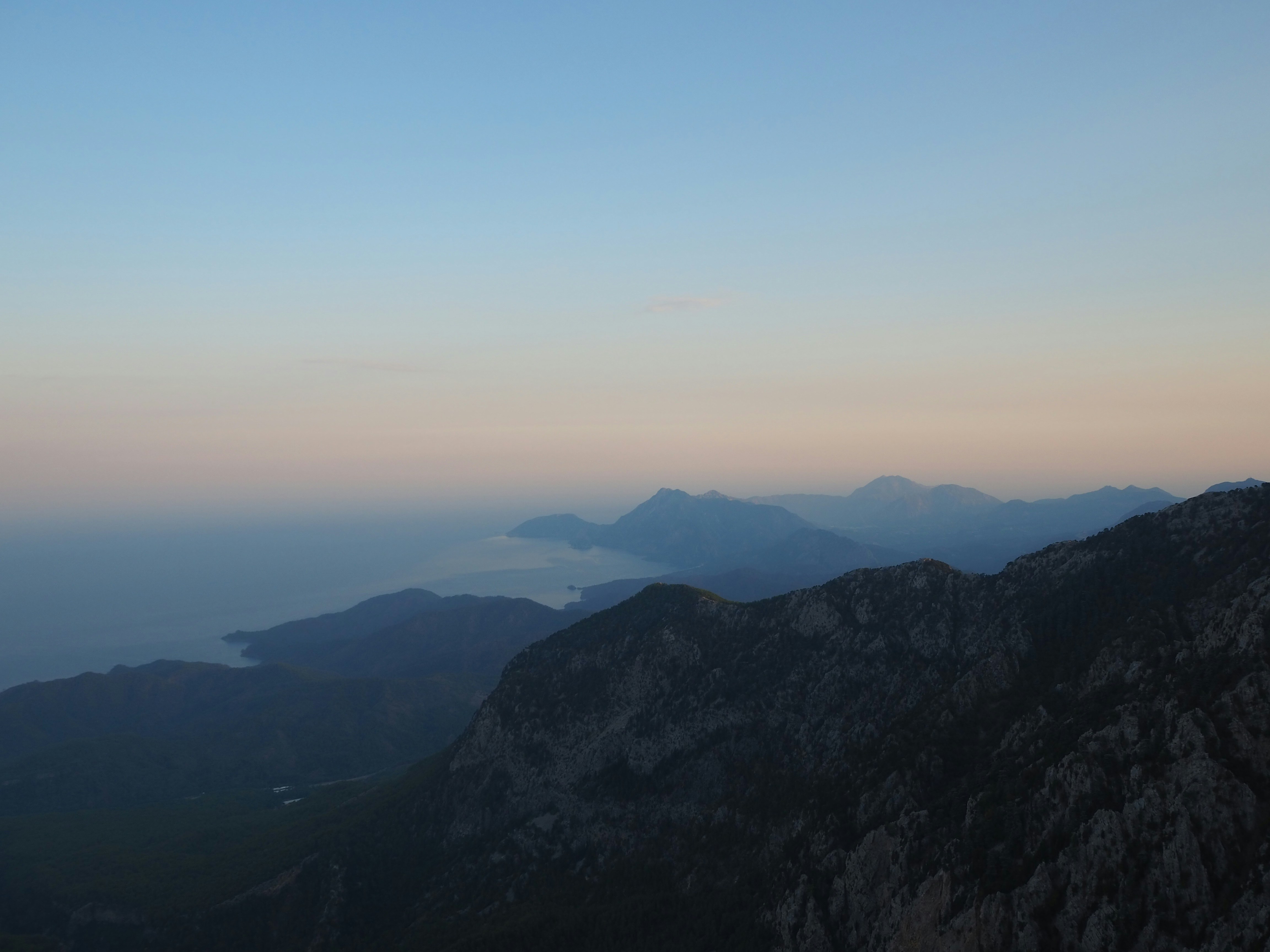 Distant mountains silhouetted against a pastel twilight sky by the sea.