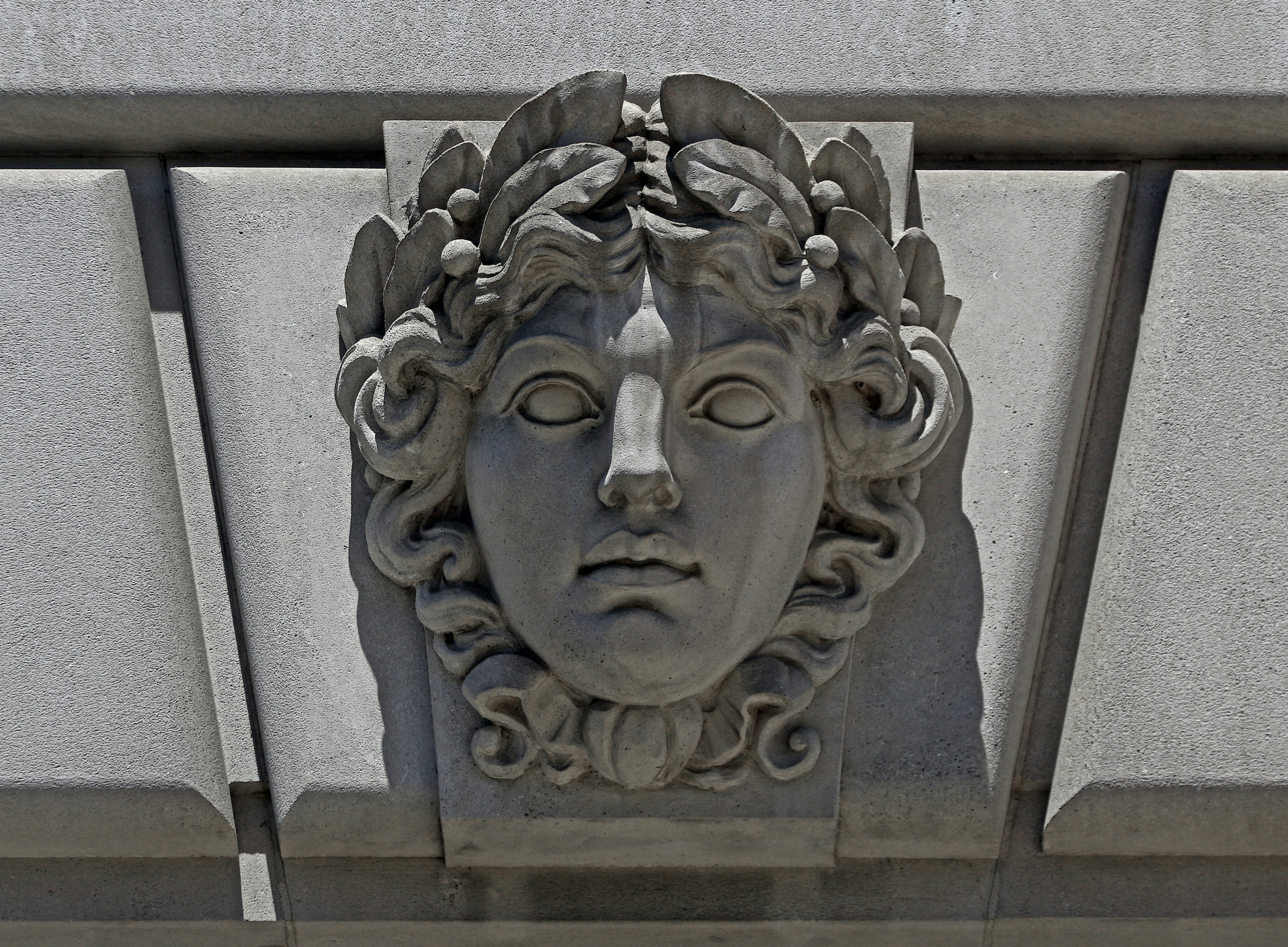 Intricate stone relief depicting a classical face adorned with laurel leaves, showcasing detailed craftsmanship and architectural elegance.