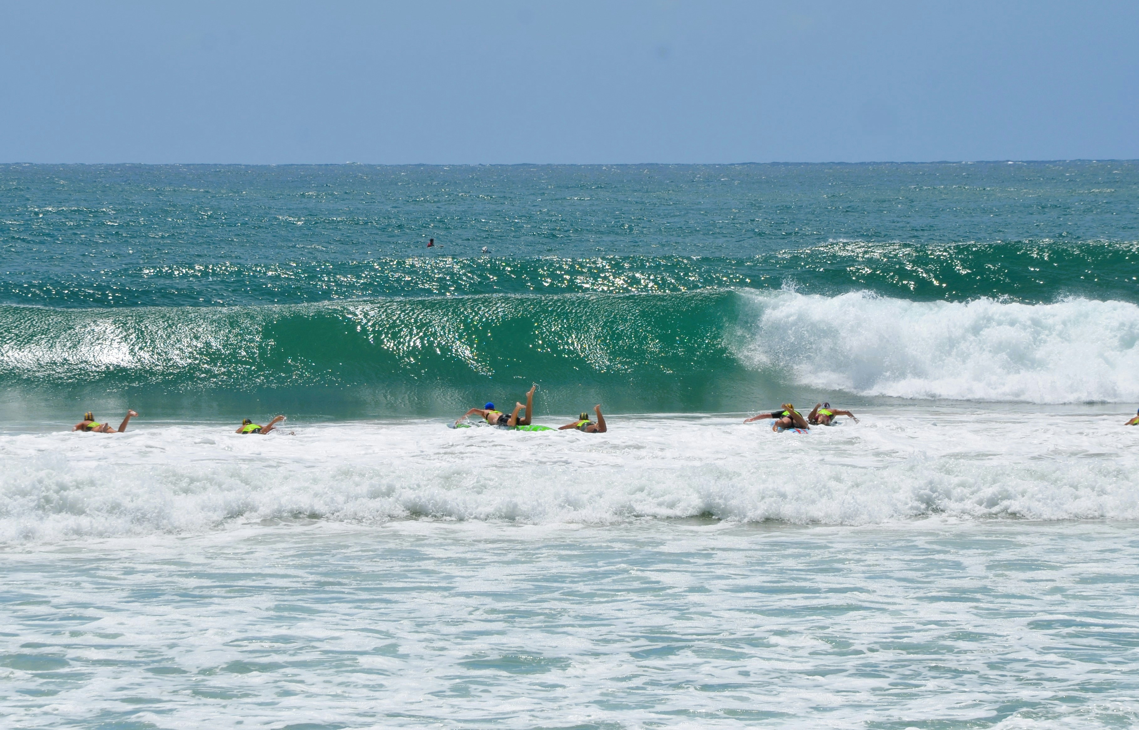 A group of people riding surfboards on top of a wave photo – Free ...